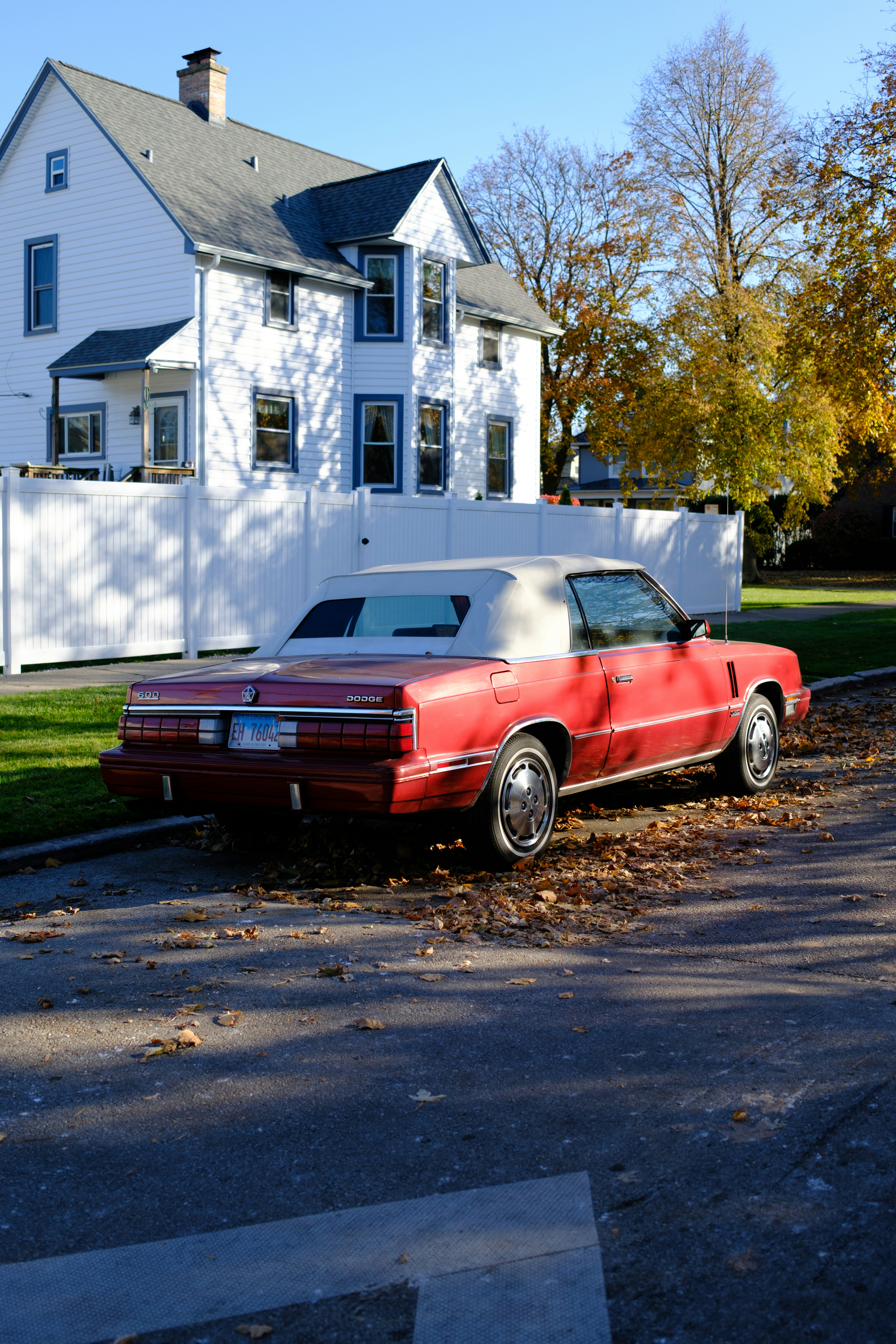 Red Convertible Under Autumn Light by a White Fenced House