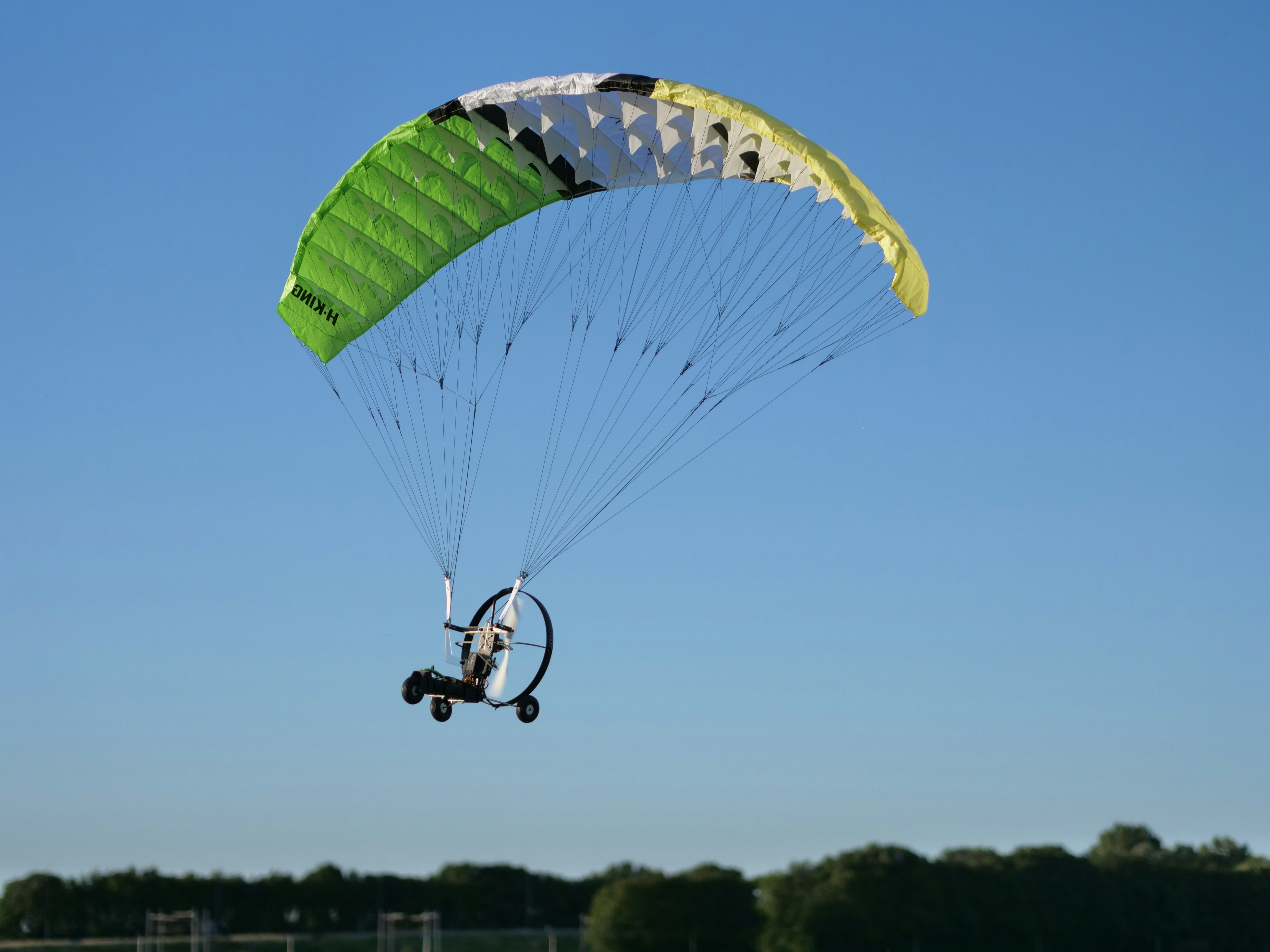 Green-White-Blue Paraglider Soaring Over Quiet Horizon