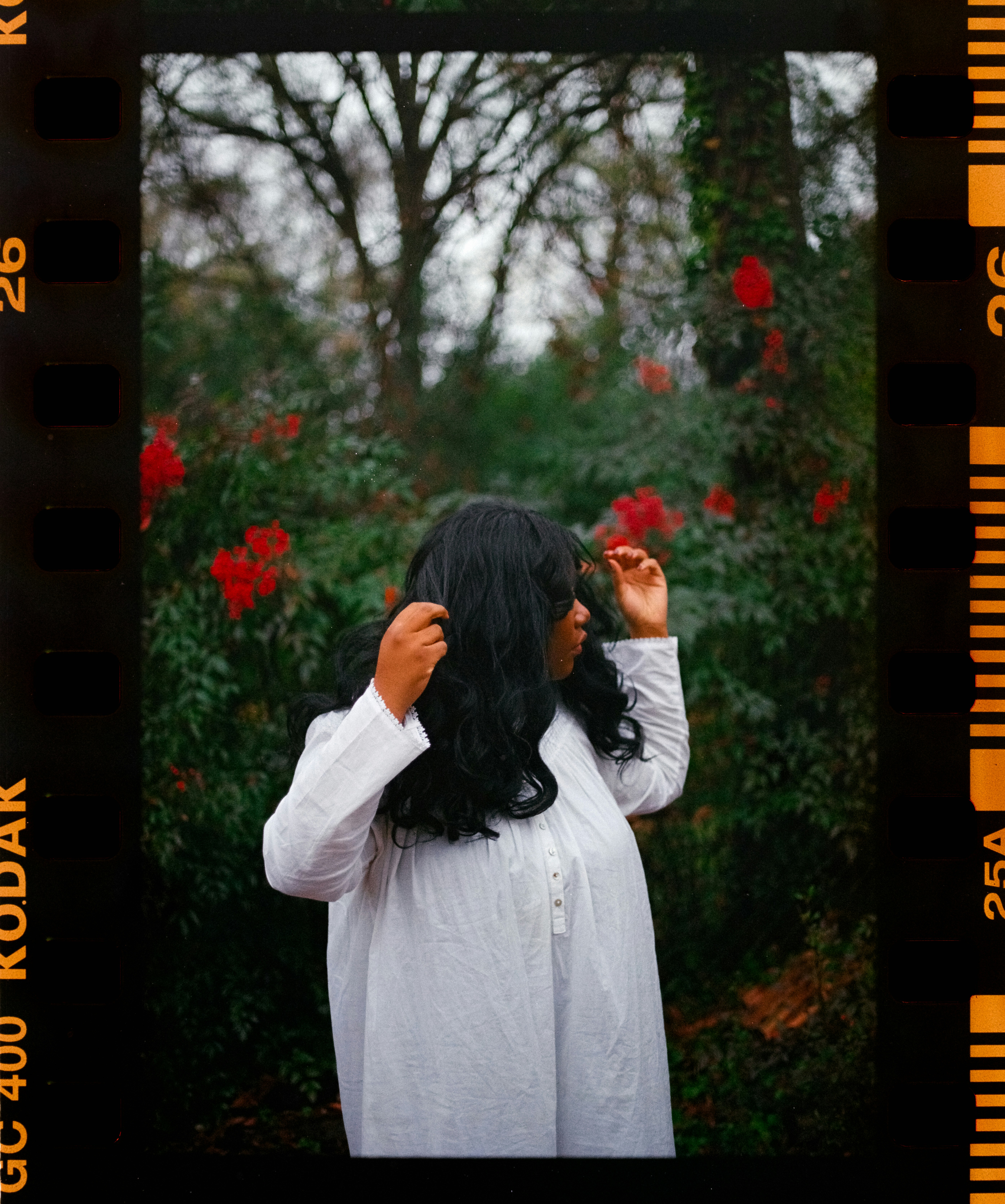Portrait in a Garden Frame: Dark Curls and White Shirt Amid Red Blooms