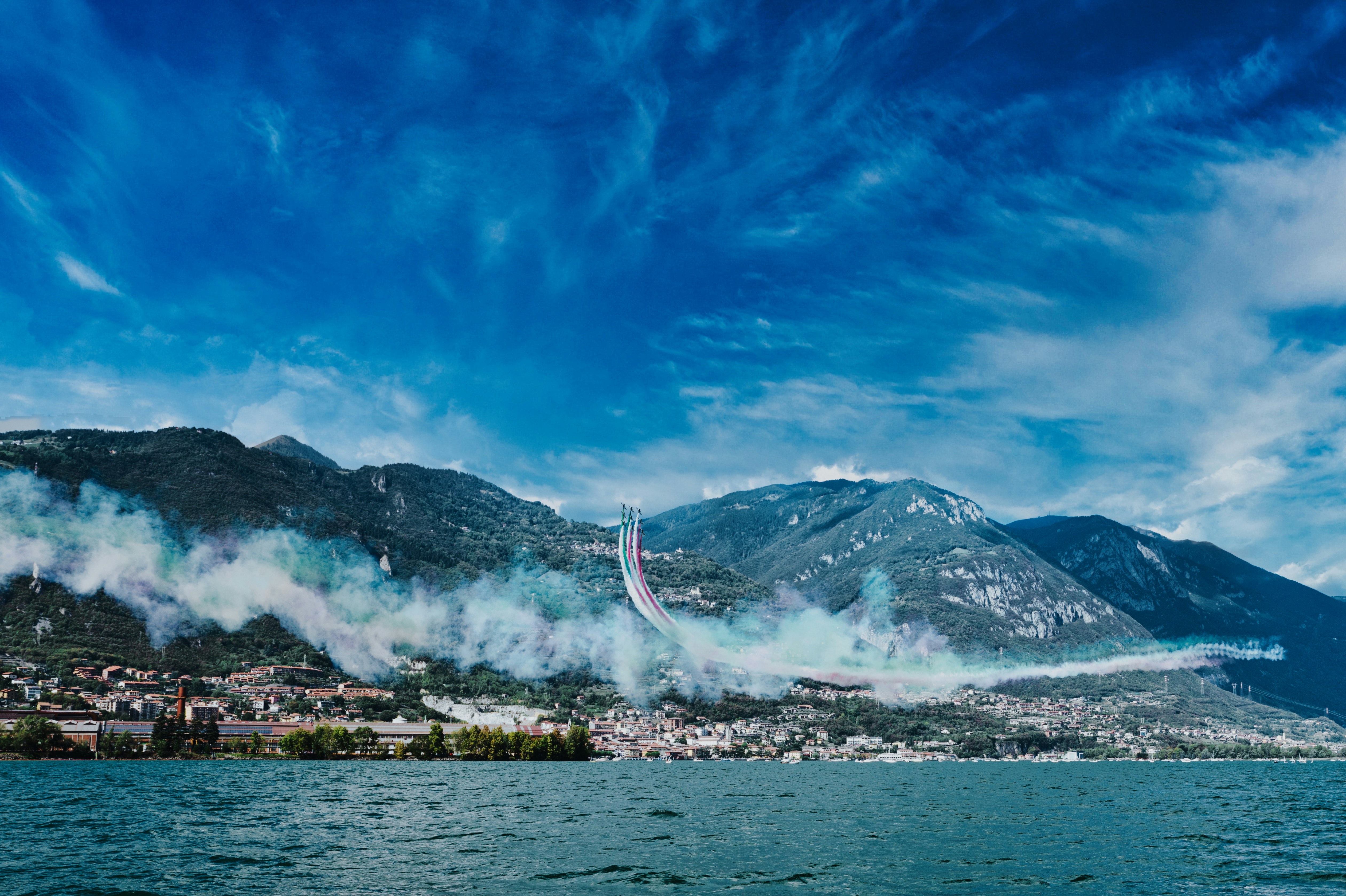 Clouds over the Lake: Smoke Trails and Distant Town Beneath Alpine Sky