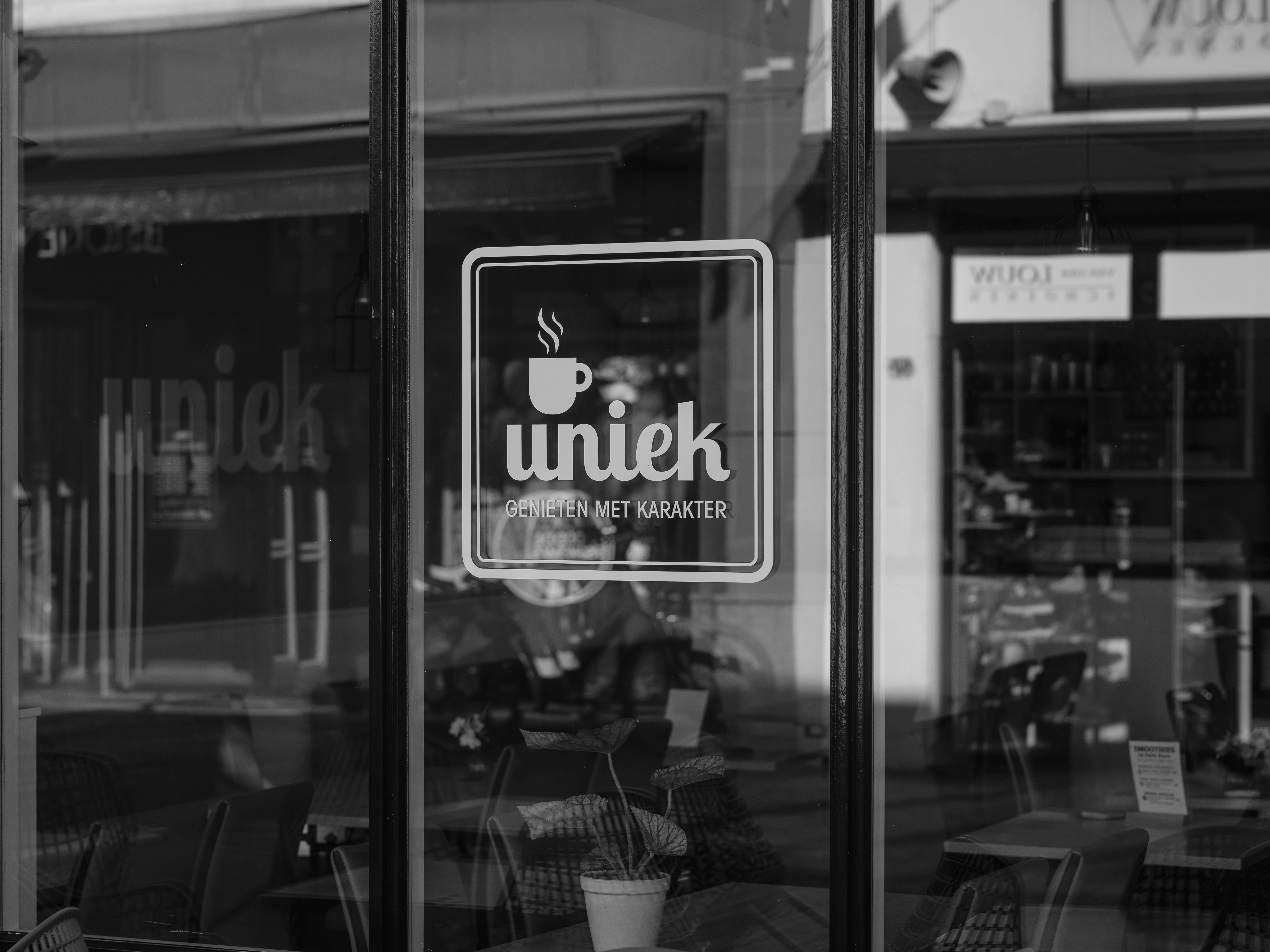 Black-and-white storefront window with a central logo sign reading 'wunek' framed by a coffee cup icon; interior seating and reflections create layered depth without color.