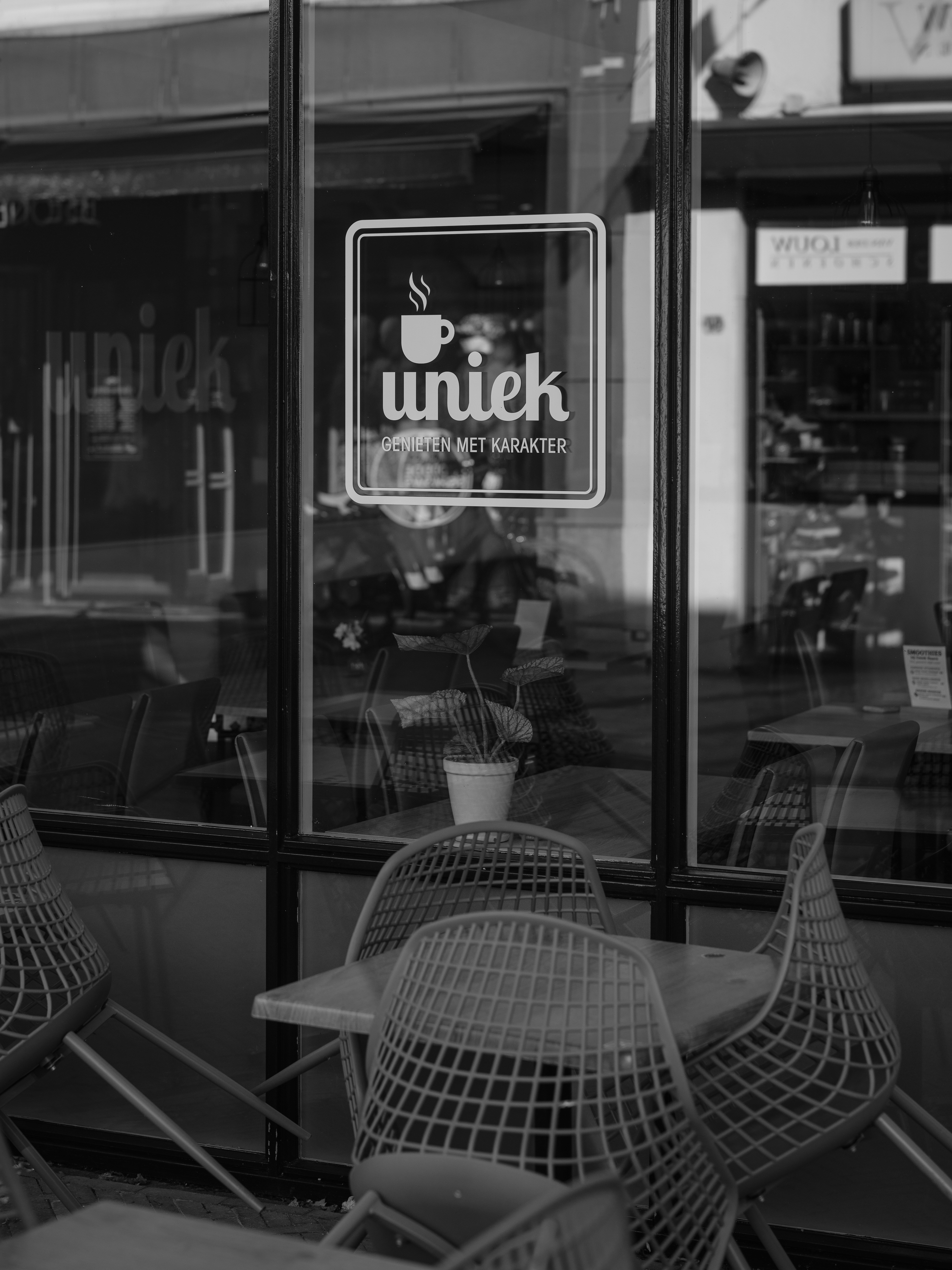 Café Window Portrait: Uniek Signage and Empty Chairs Through Glass