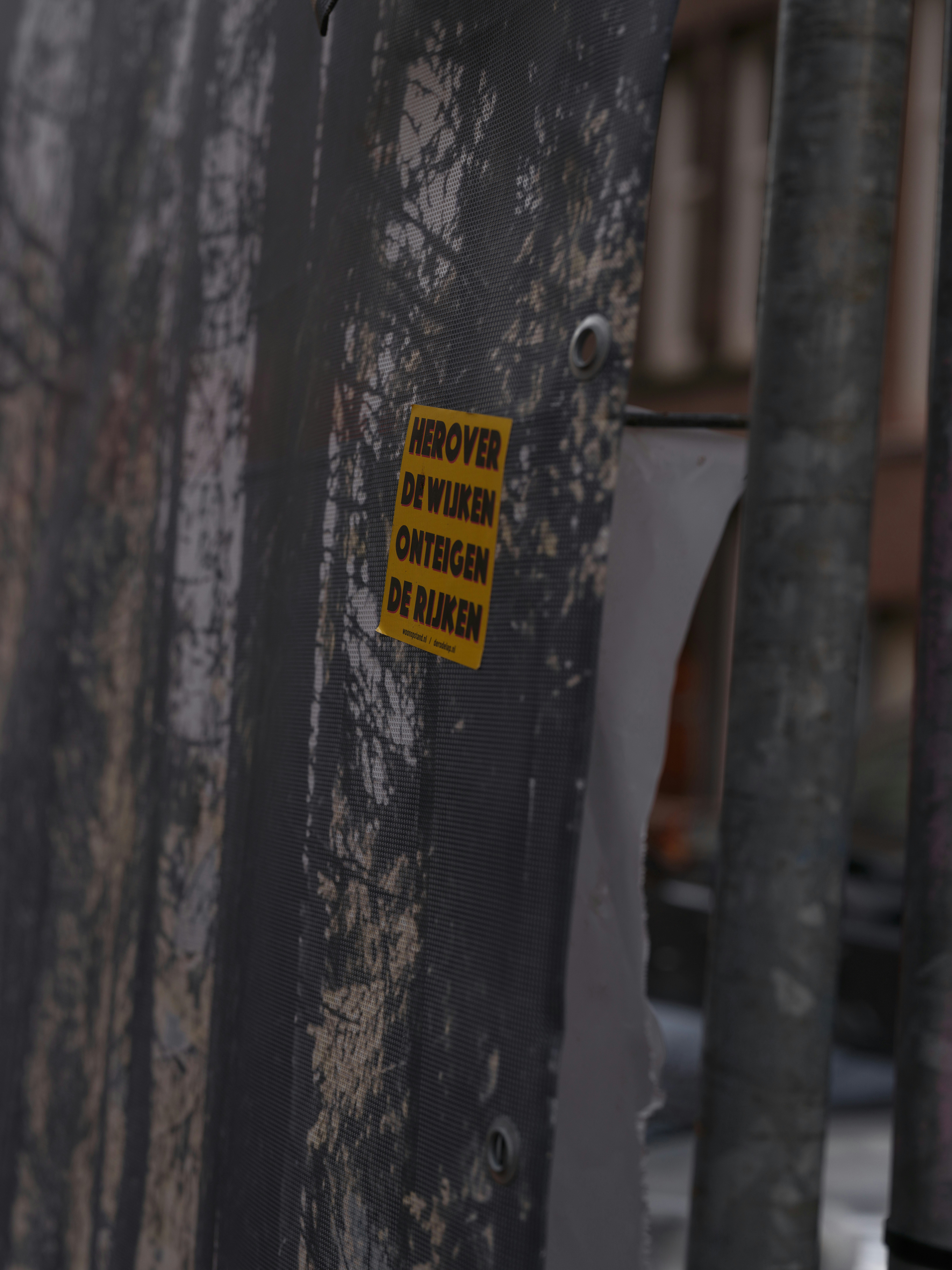 Yellow warning sticker on worn mesh near scaffolding