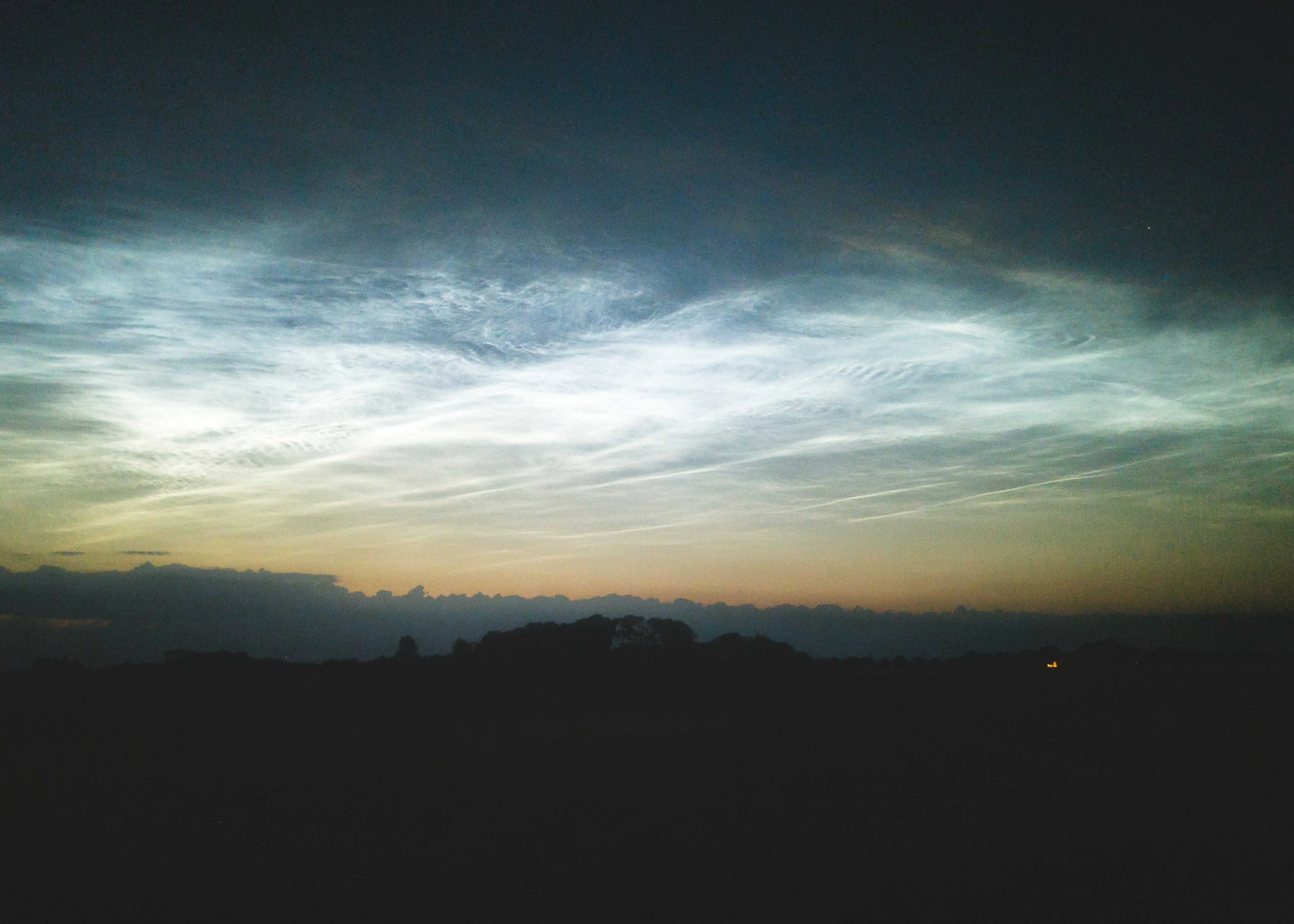 Das Bild zeigt einen dramatischen Himmel mit feinen, faserigen Cirruswolken in Pastelltönen von Blau, Rosa und Orange während eines Sonnenuntergangs oder der Dämmerung. Der Horizont ist dunkel, mit leichten gelben Akzenten, typisch für hohe Eiskristallwolken bei abendlichem Licht.