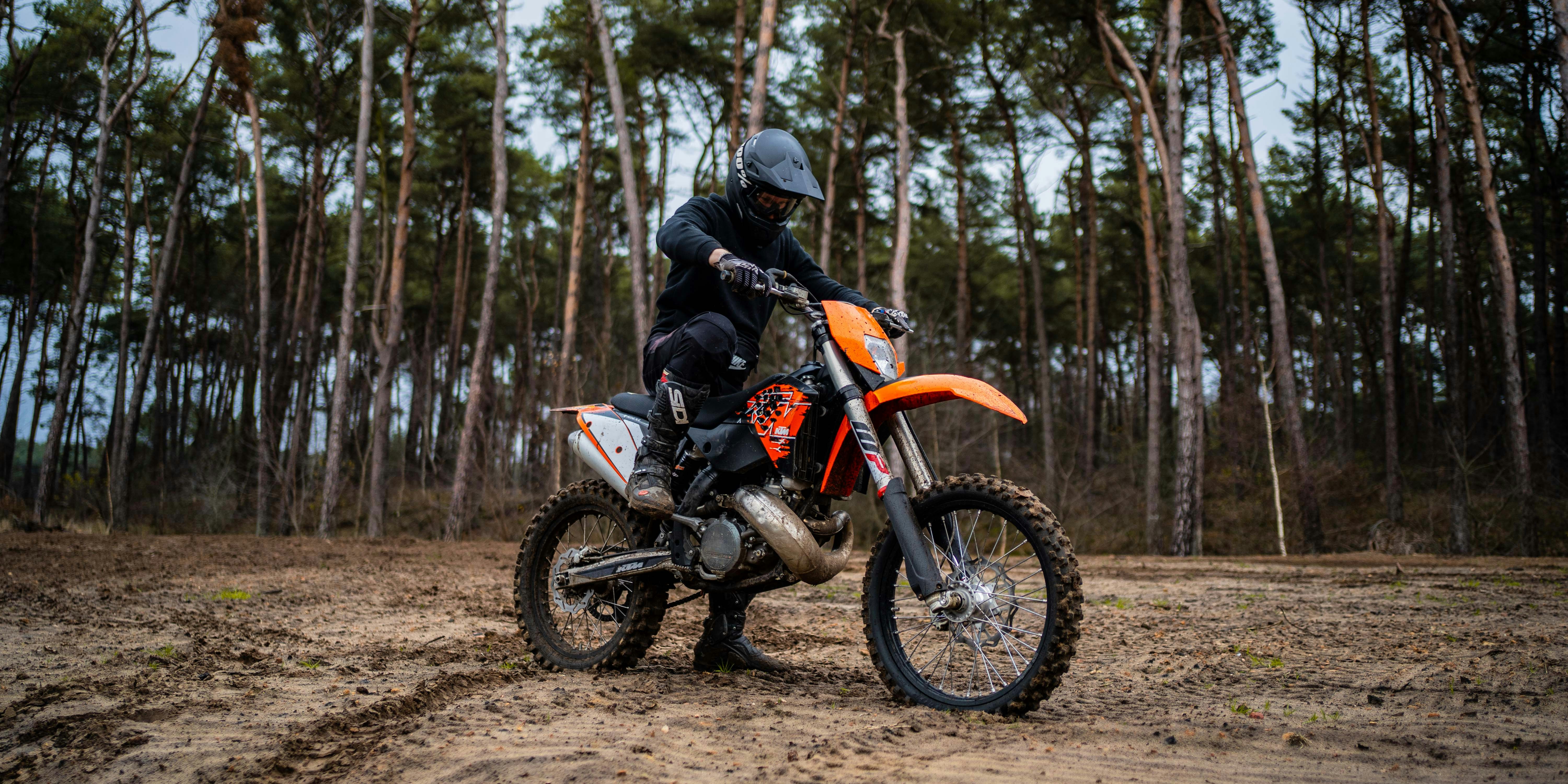 Orange KTM dirt bike riding through wet and muddy forest terrain. Offroad enduro training session in natural light.