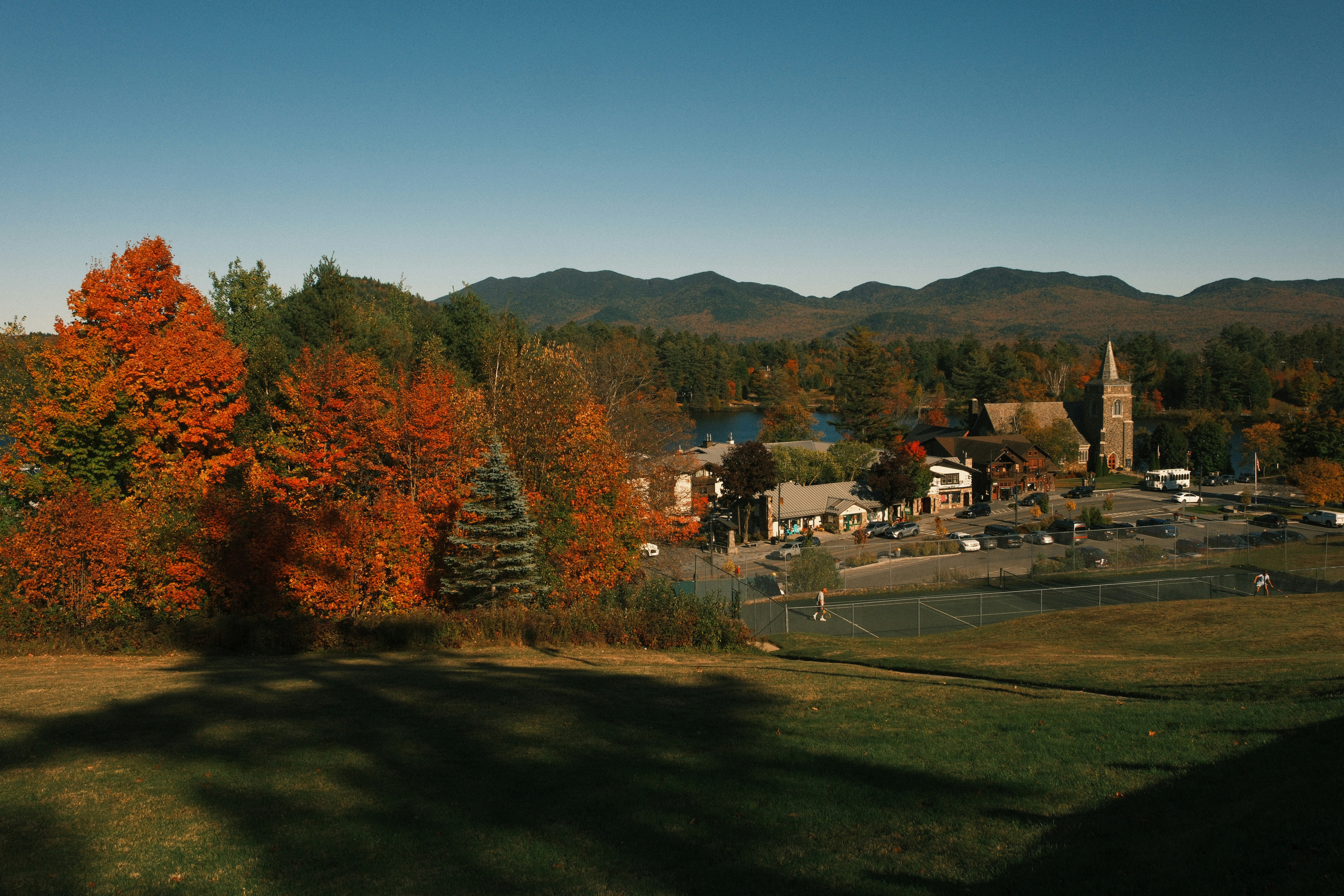 Scenic fall view of a mountain town with colorful autumn trees, a church tower, and a lake in the background. A warm and peaceful landscape showcasing peak fall foliage.