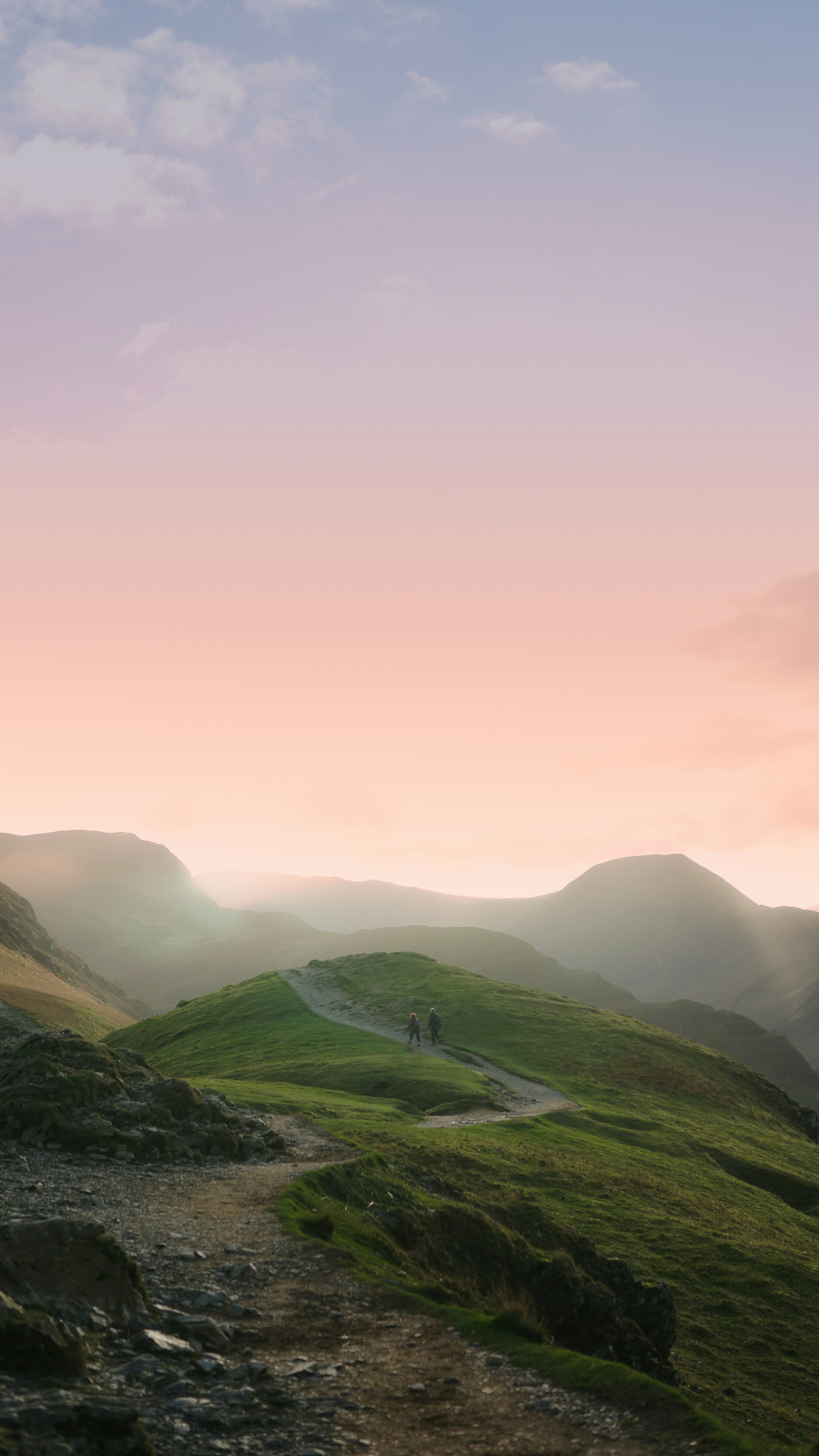 Hikers on a trail through rolling green hills at sunset.David Lam