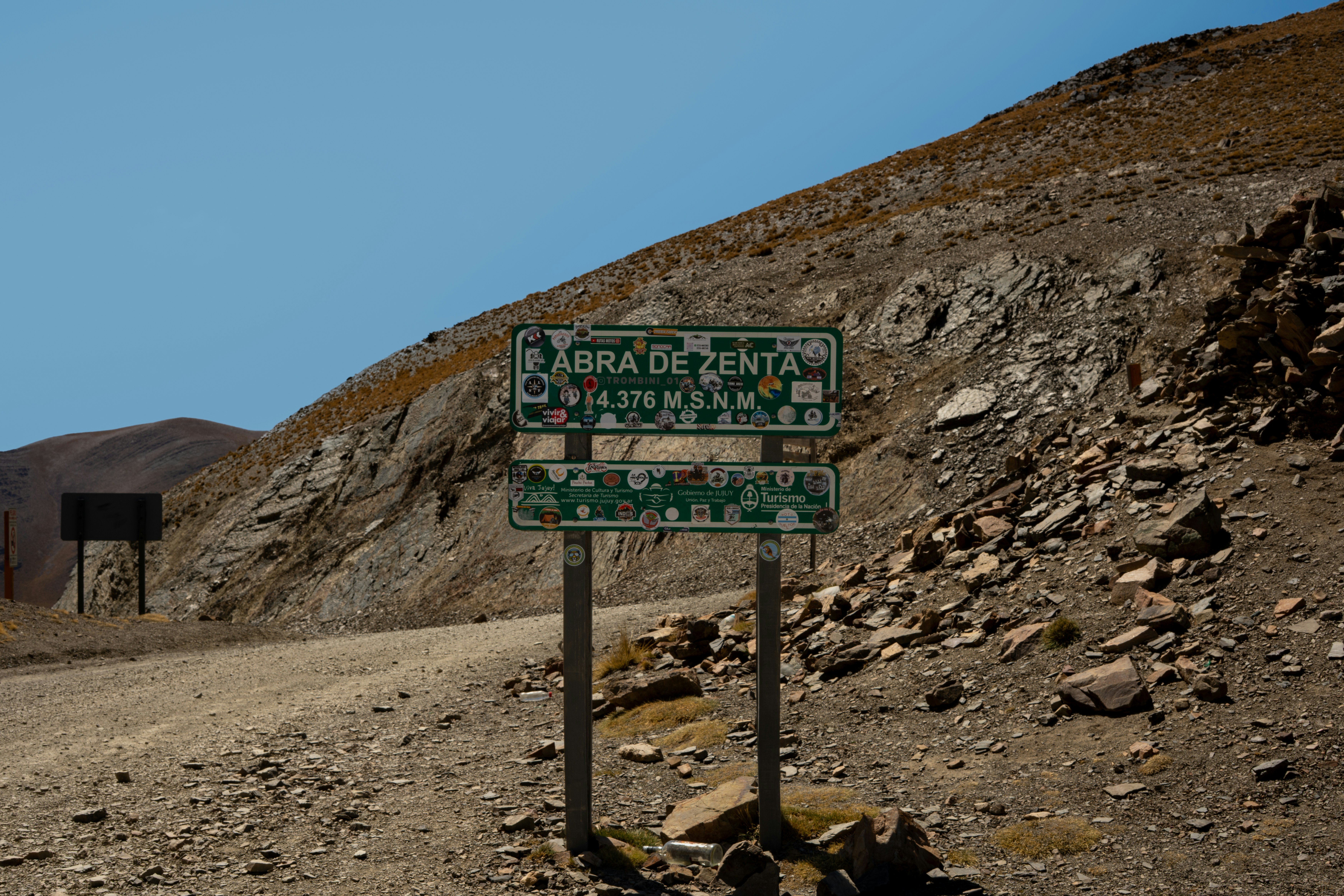 Sign marking the high mountain pass of Abra de Zenta at 4,376 meters above sea level, standing against a dramatic high-altitude landscape.