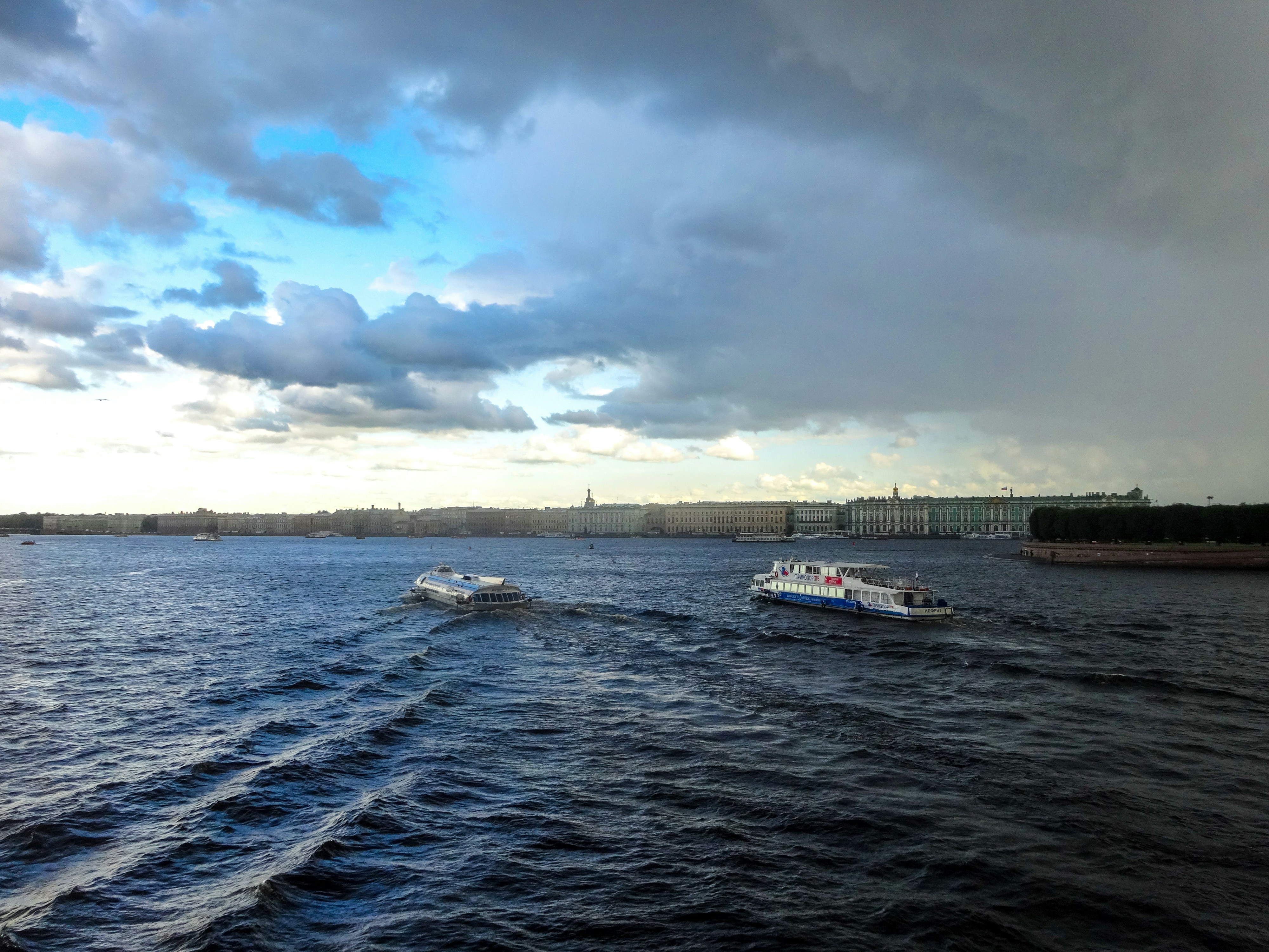 Towboats carving wake across a broad river under turbulent skies