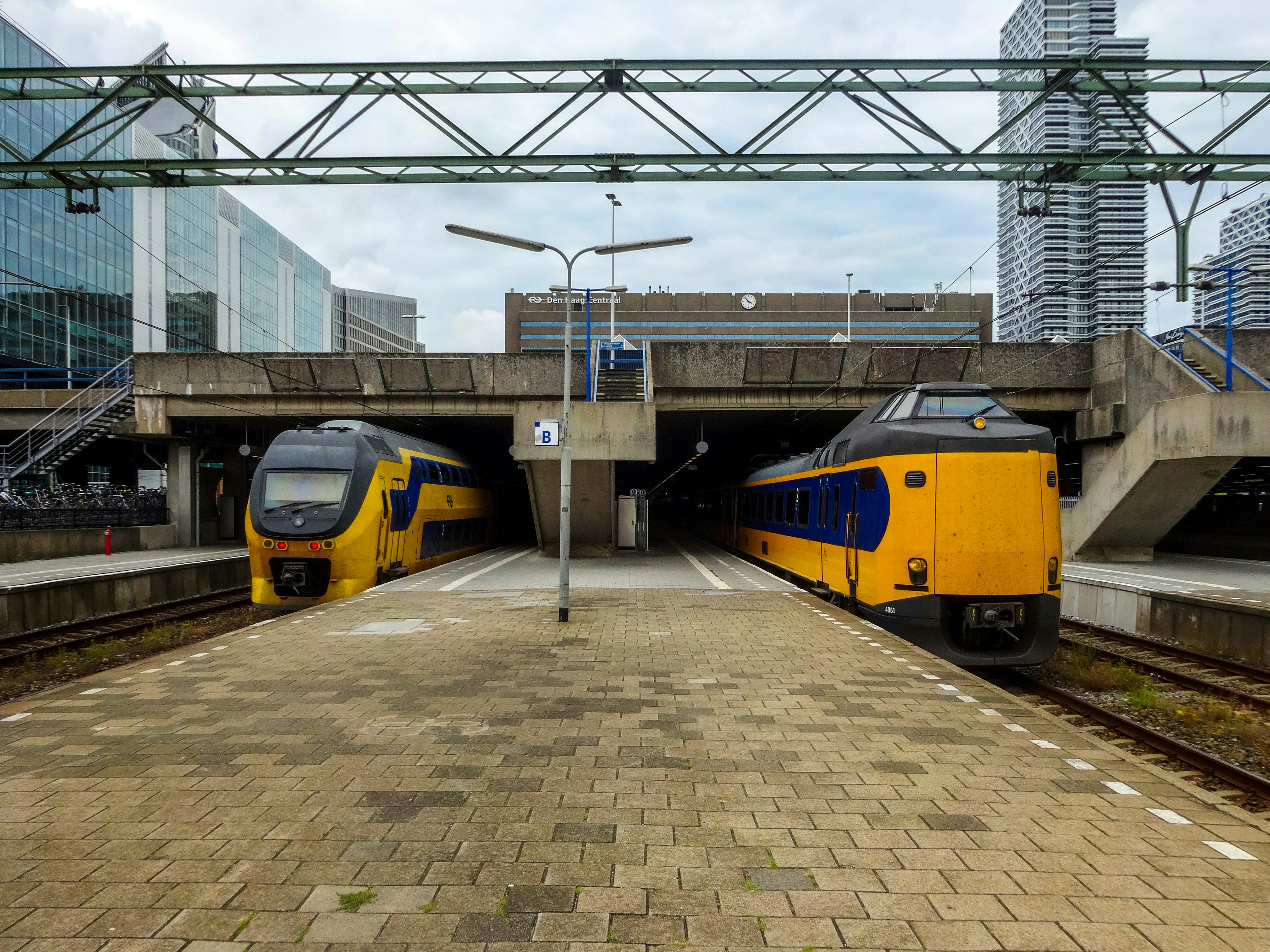 Two yellow trains at a station under bridge