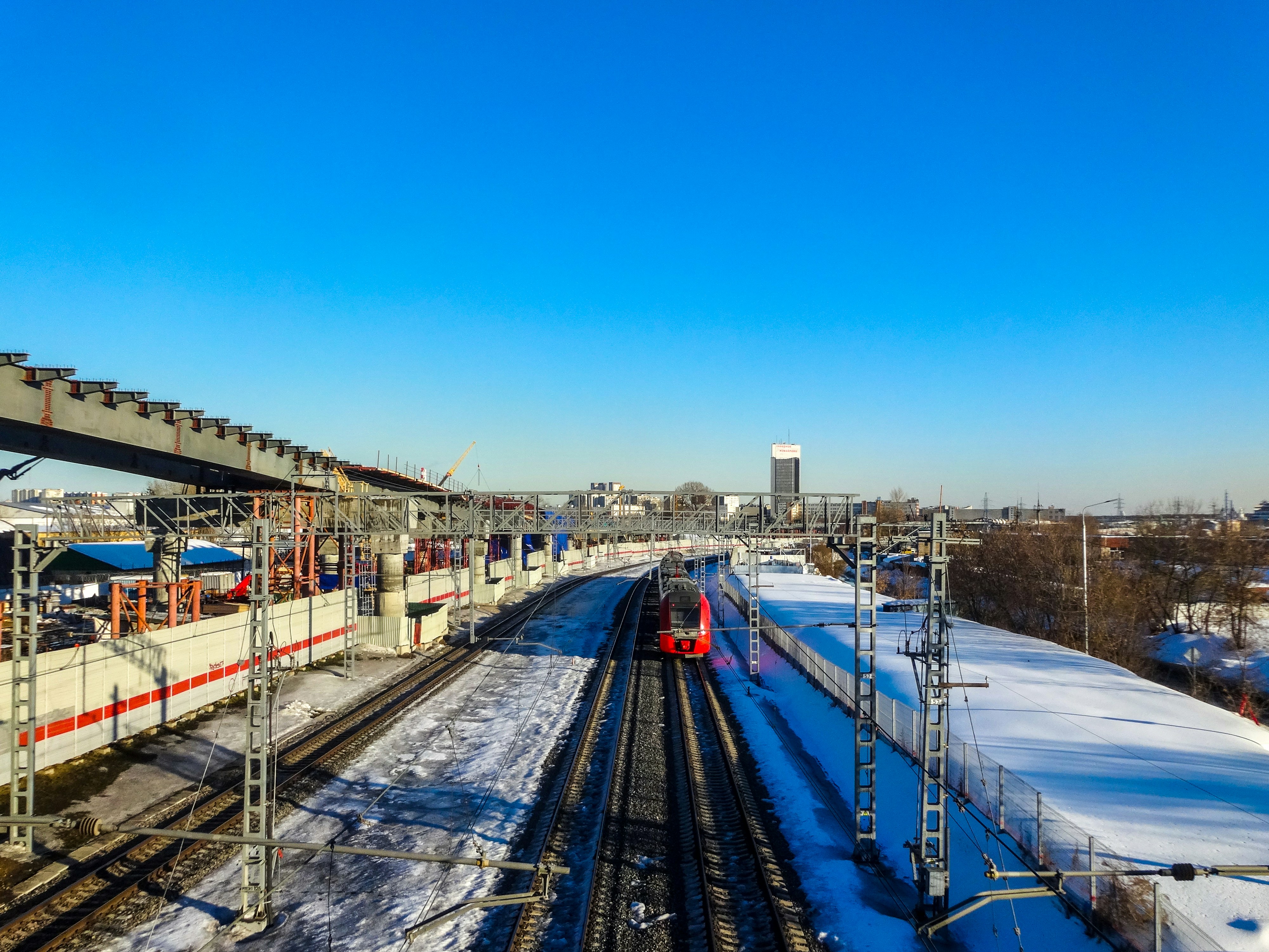 Red locomotive slicing through a snowy urban rail yard at midday