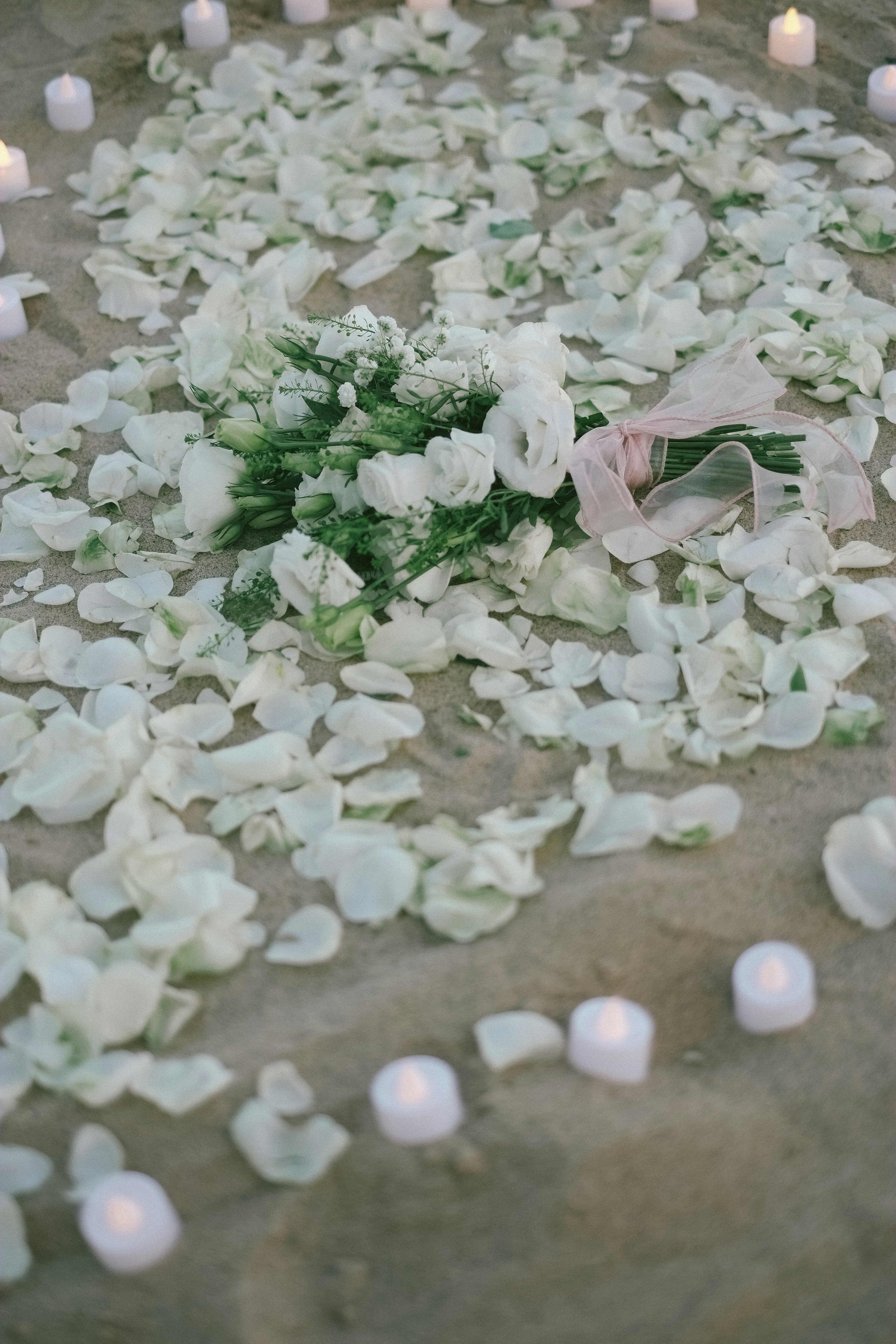 Petals at the Altar: A Bouquet of White Blooms on Sand with Candlelight