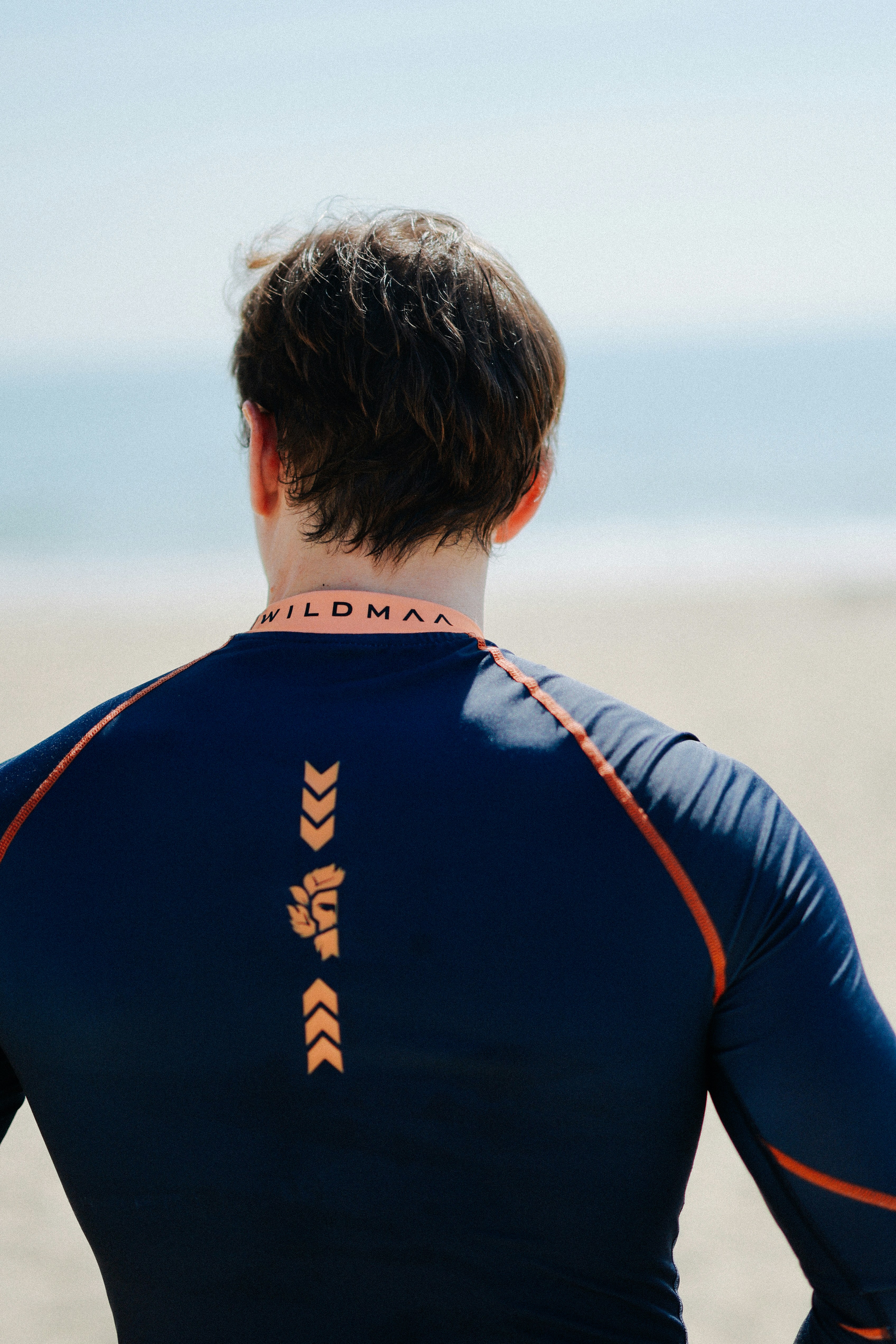 Back of a surfer’s jersey at the shoreline, a quiet beach session begins