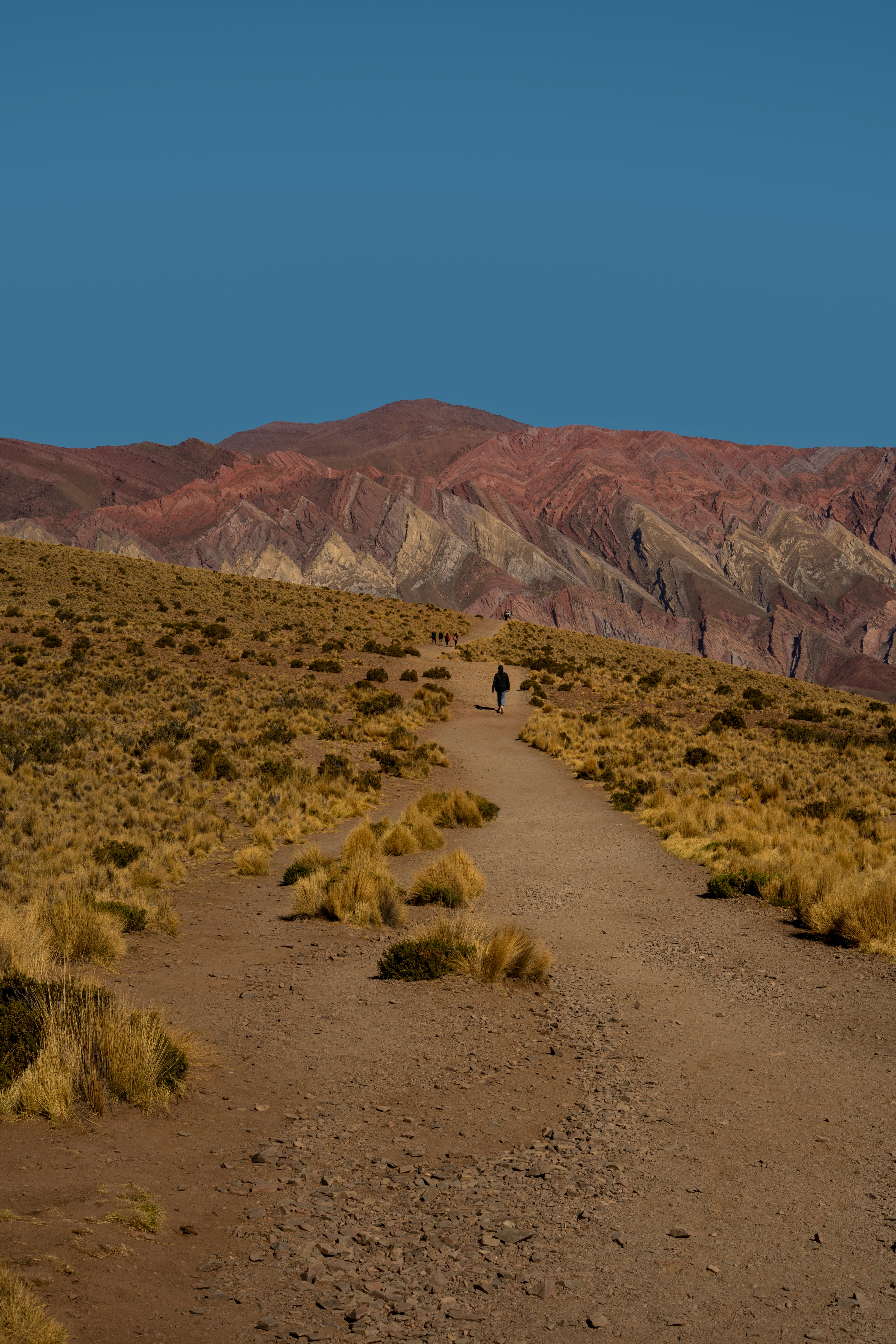 A person making their way through rugged mountain terrain, surrounded by dramatic colors and sweeping views.