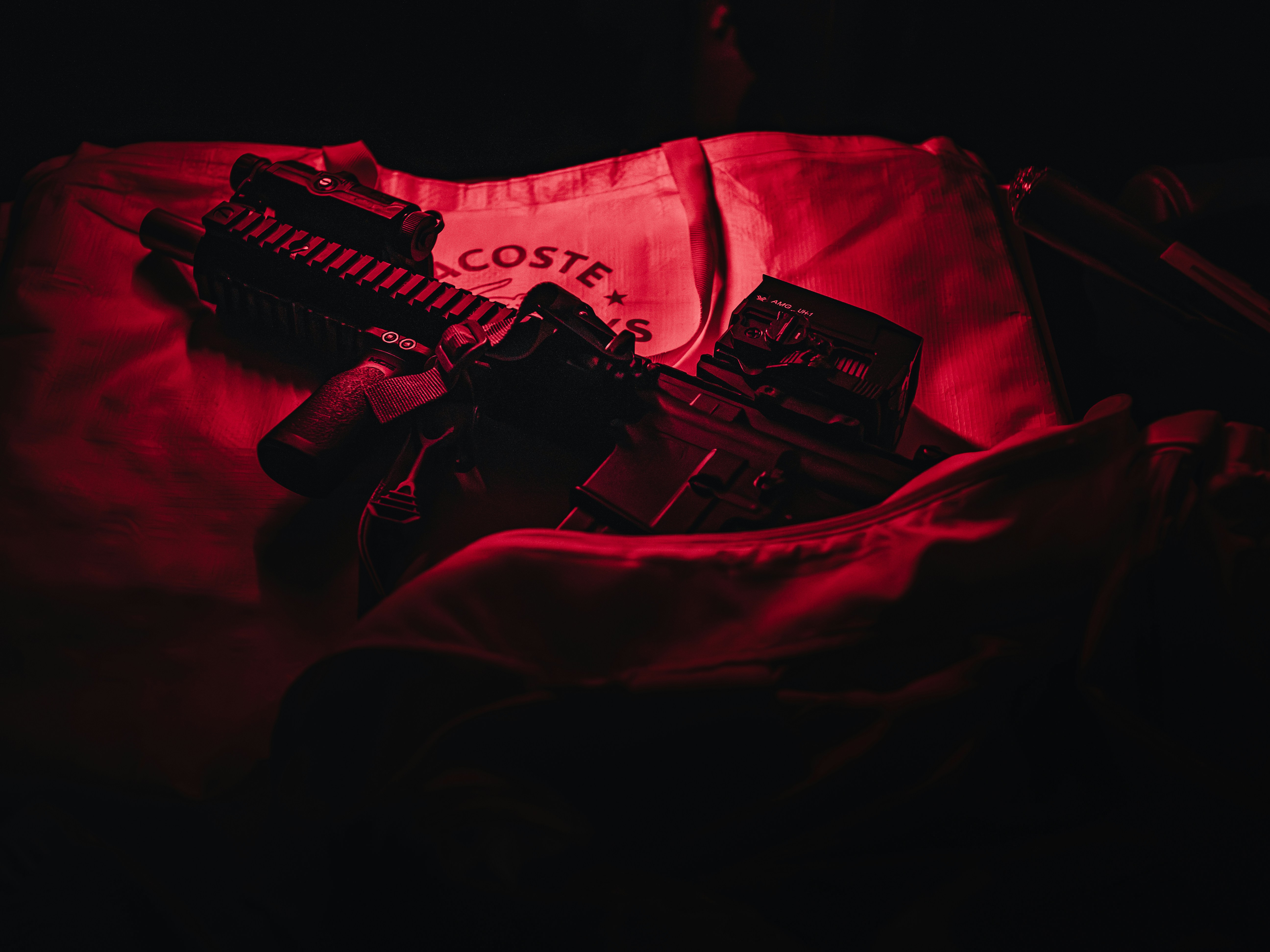 Assault rifle resting on red fabric with lacoste logo.