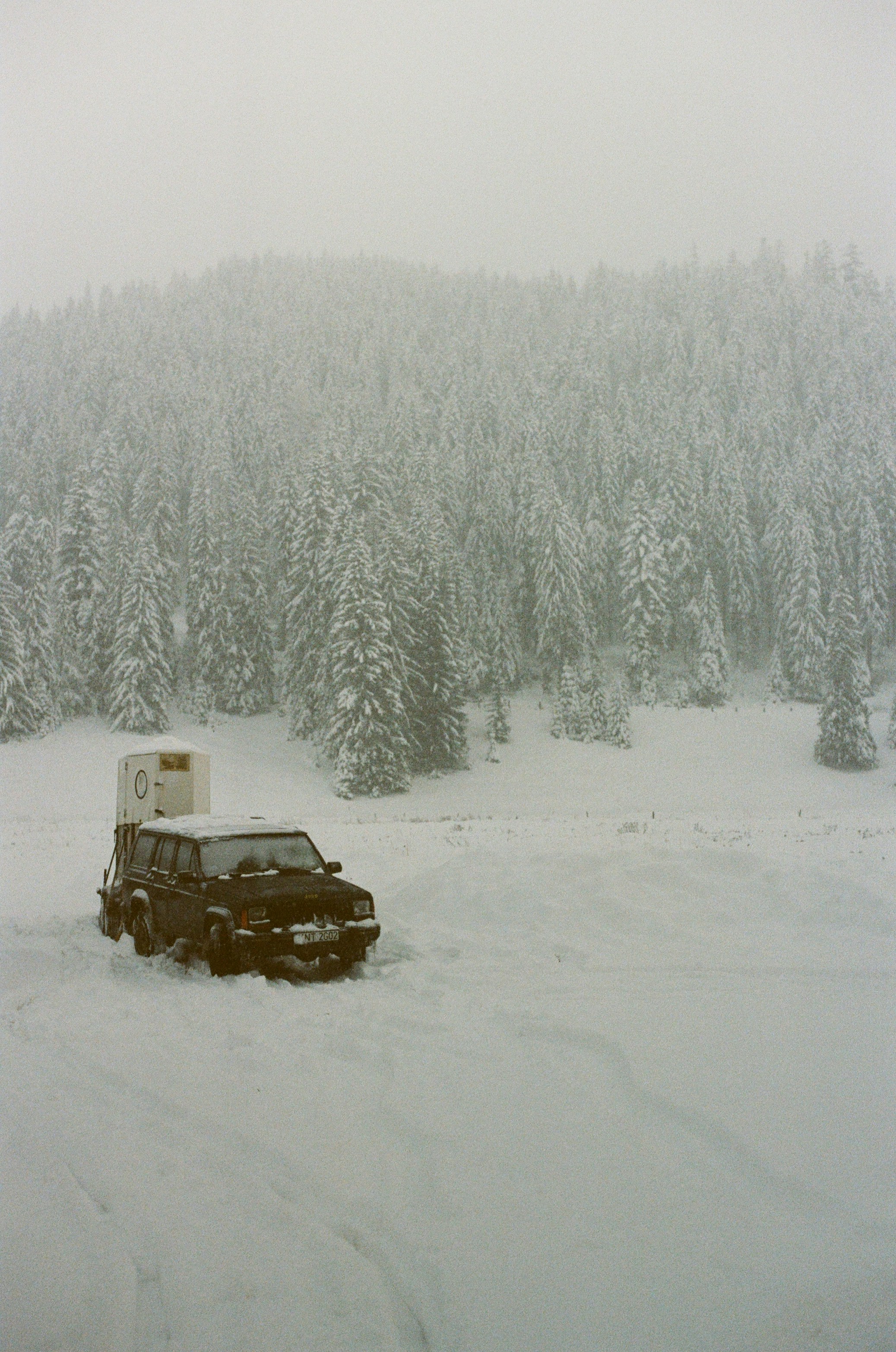 A vehicle and trailer in a snowy forest clearing.