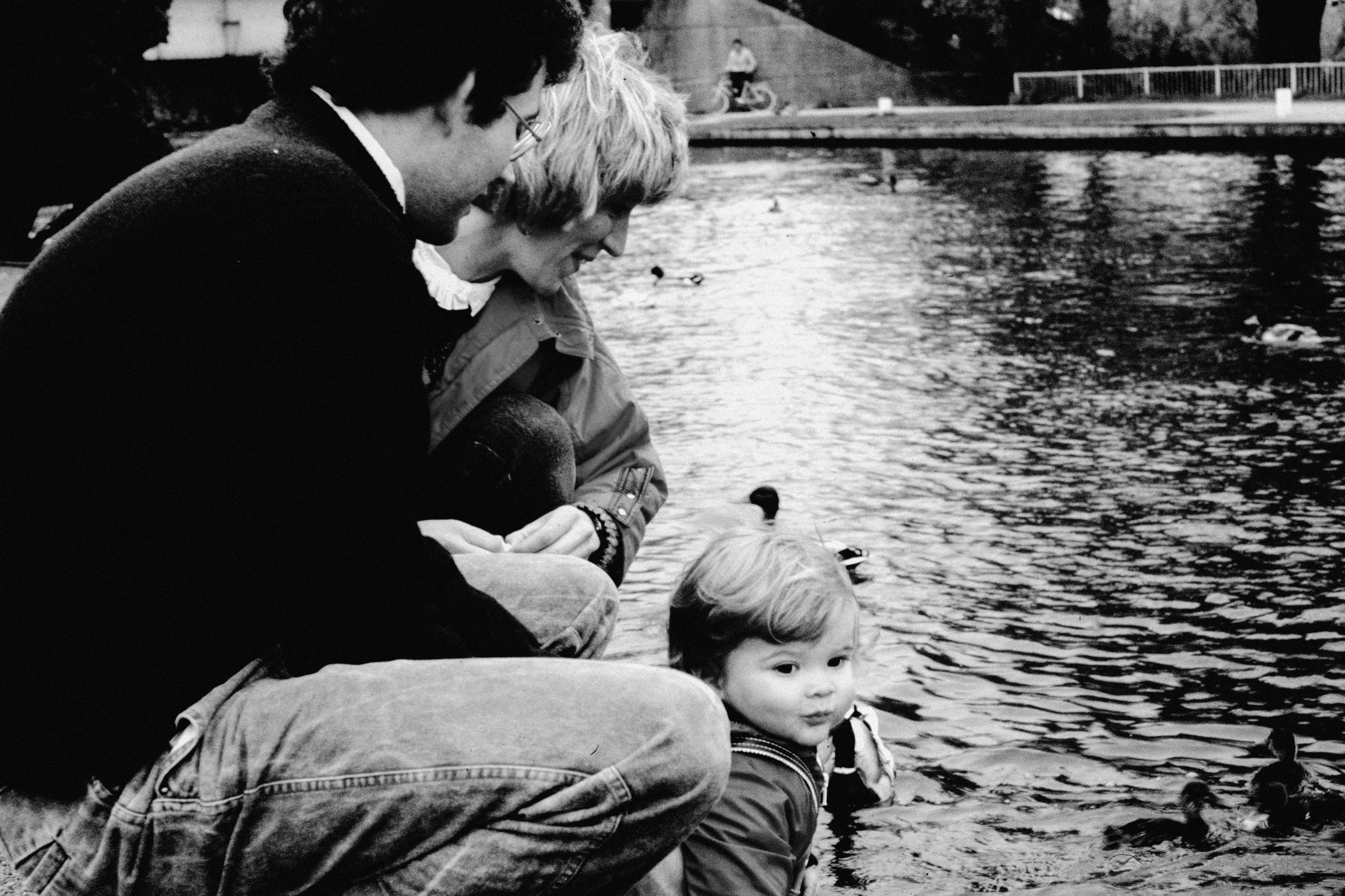 Tender Moment by the Water: Father and Mother with Child by the Duck Pond