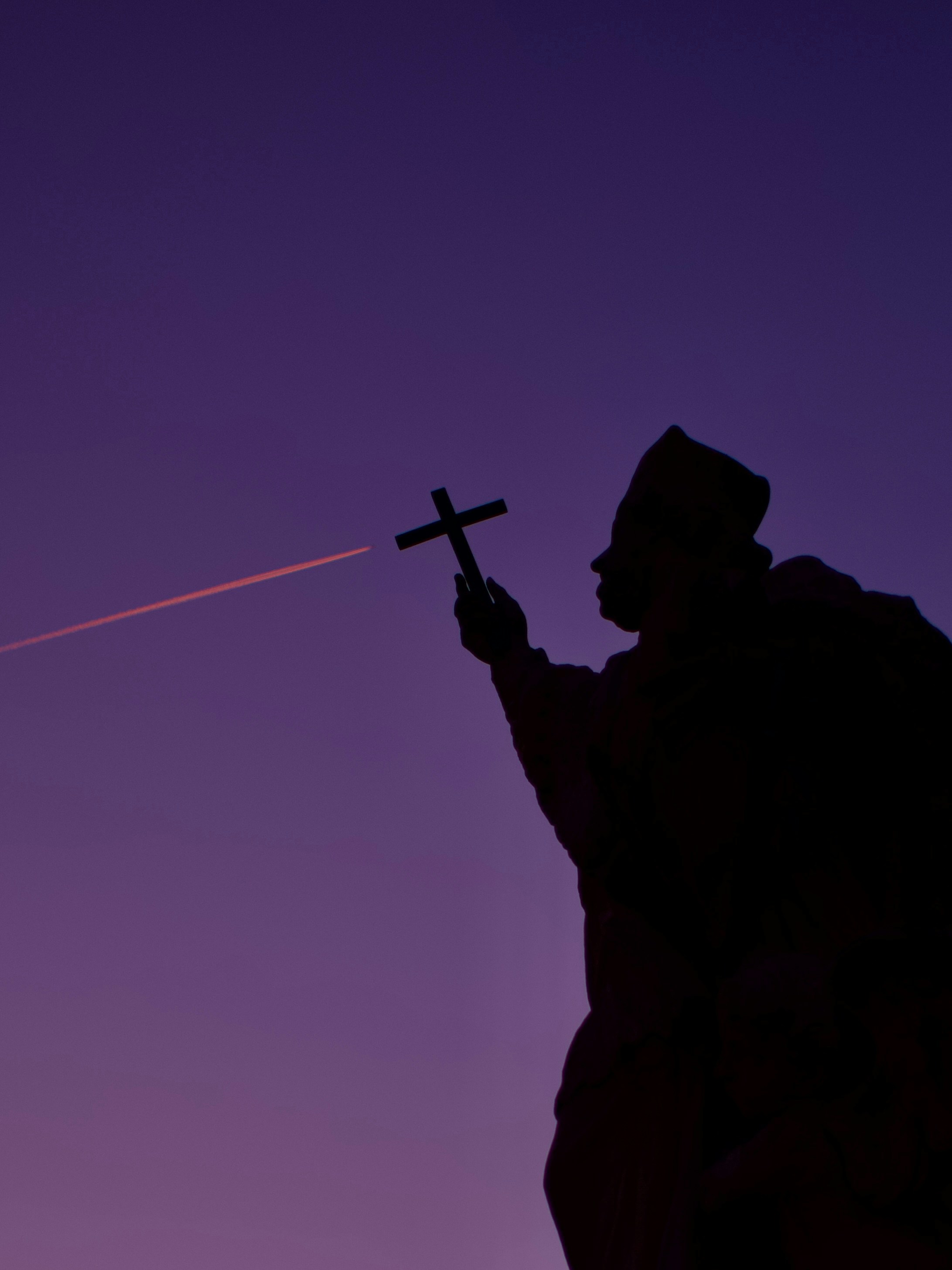 Silhouette of a Cleric with a Lanterned Cross Against Twilight