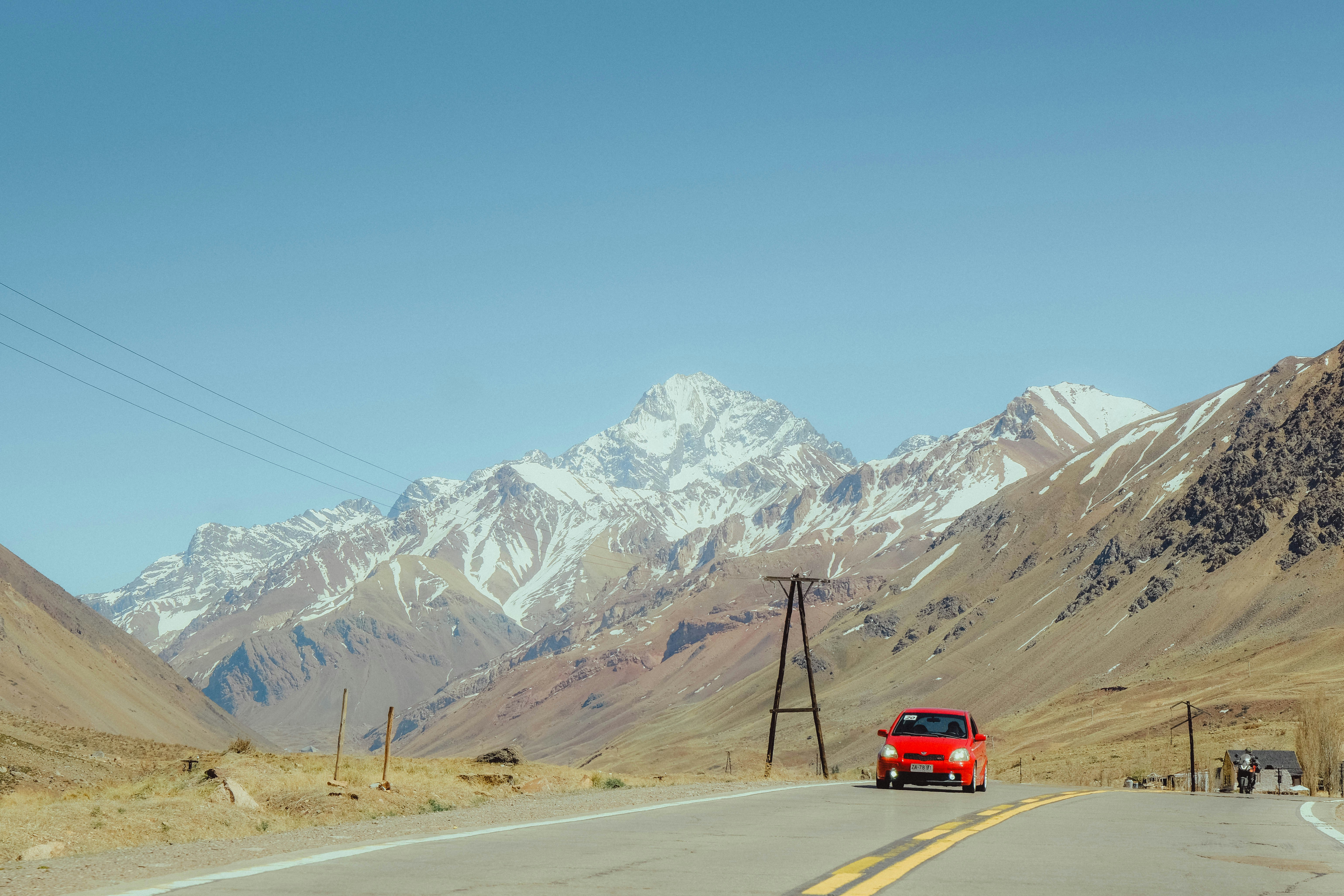 Red Car on a Desert Highway Beneath Snow-Capped Peaks