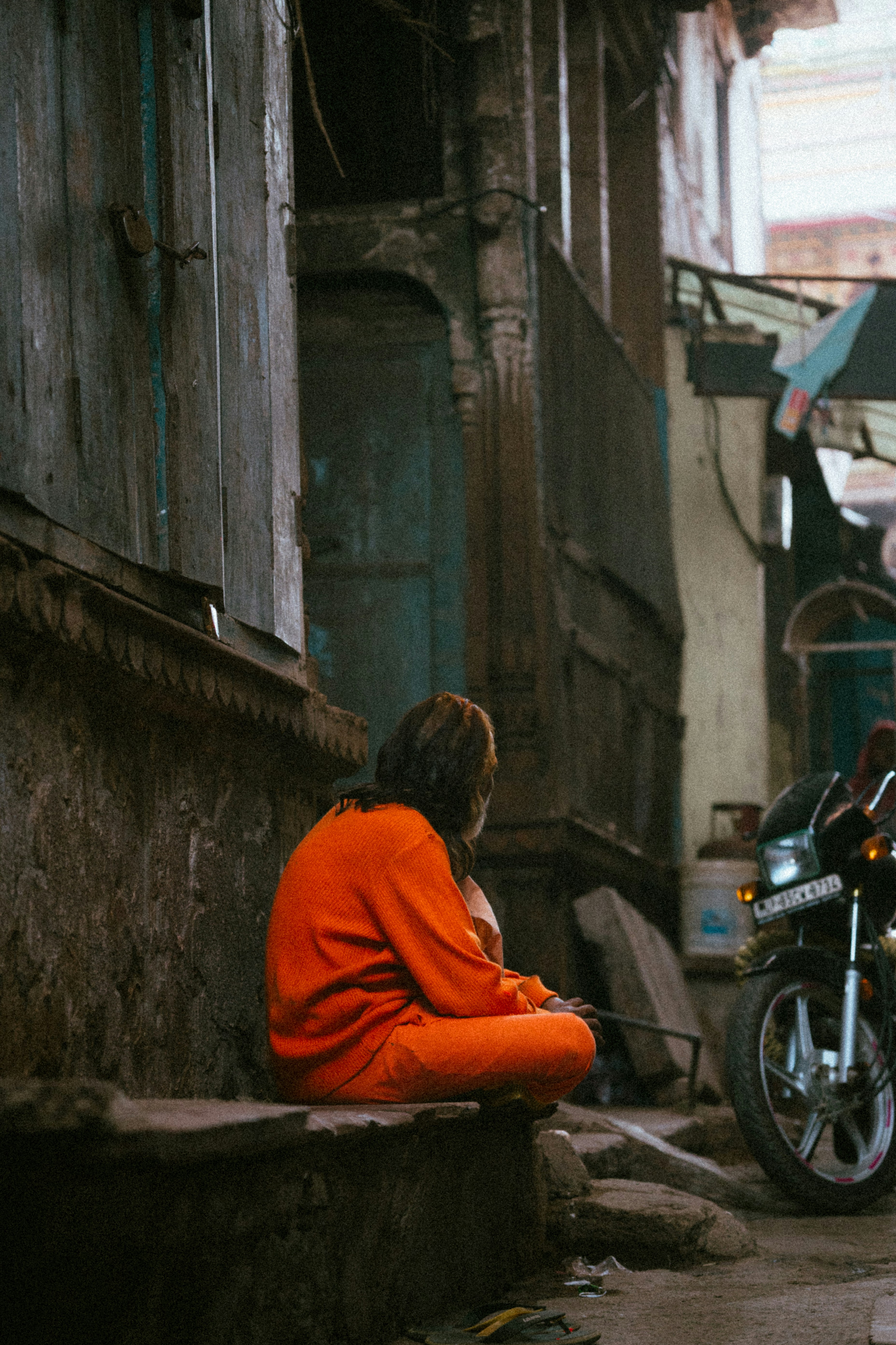 Orange-clad figure in a narrow alley overlooked by weathered facades