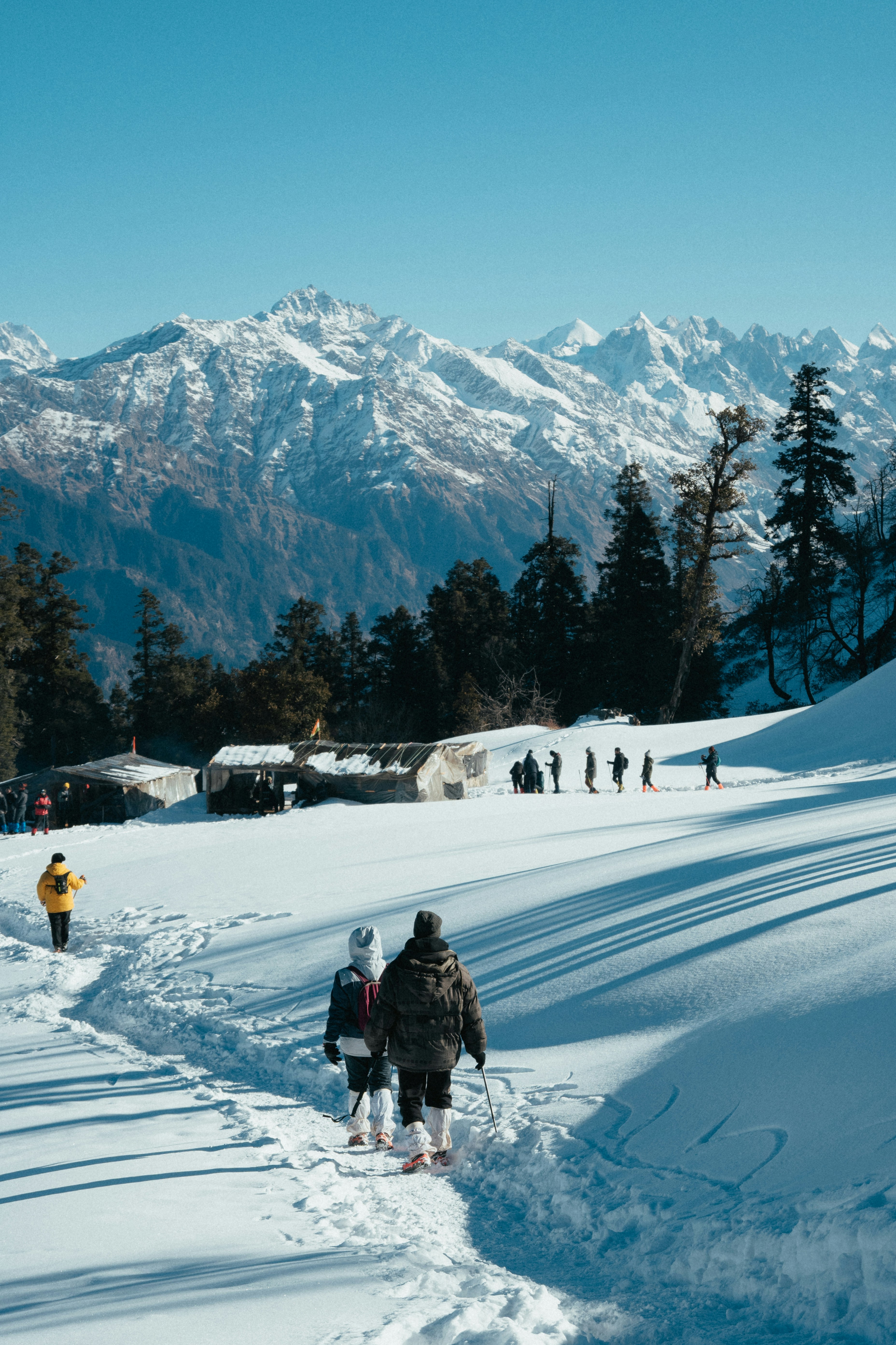 Snowbound Trail: People Trek Toward Alpine Kasbah Under A Blue Sky