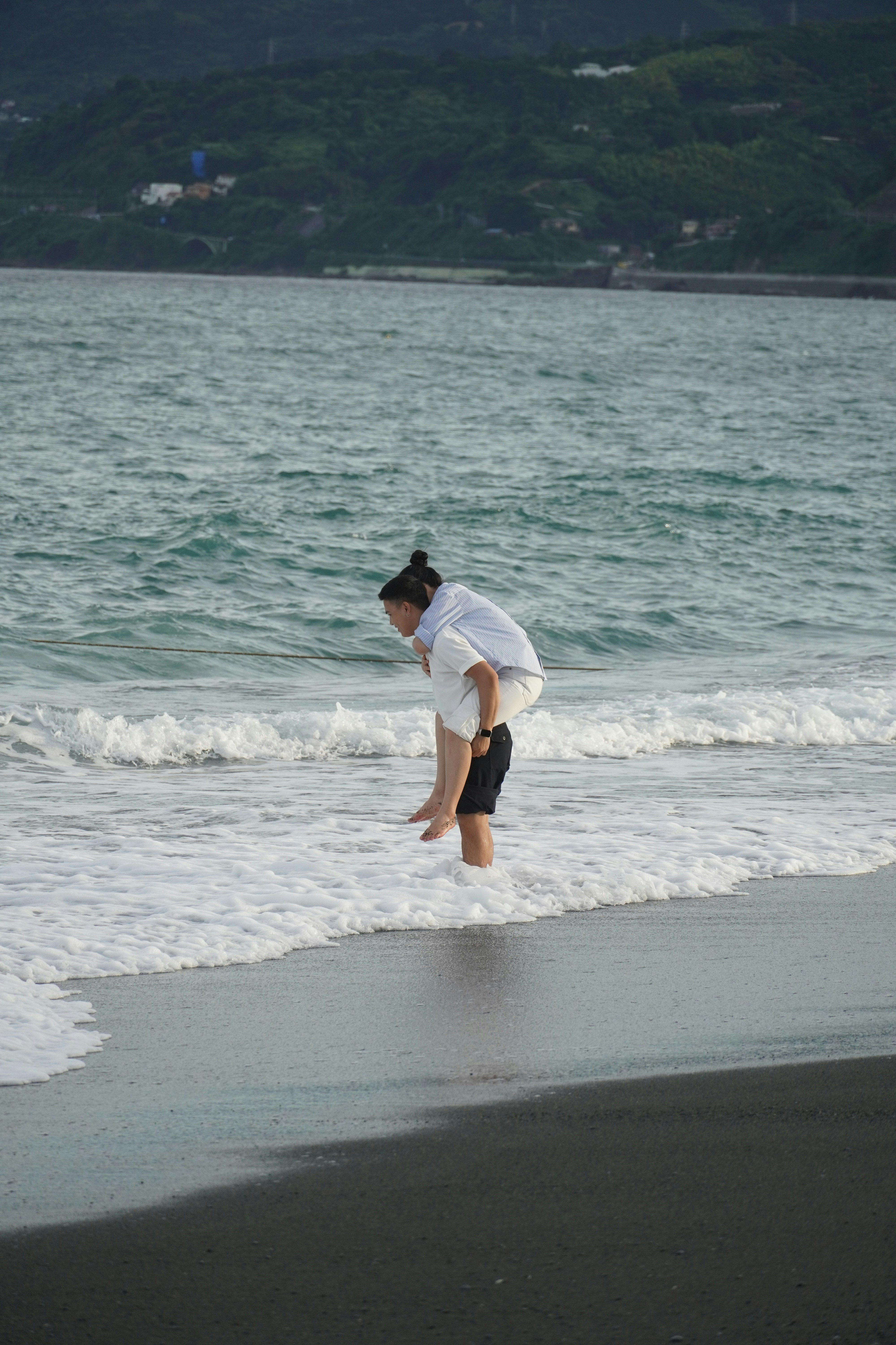 A lone beachgoer bent at the shoreline, surveying the surf