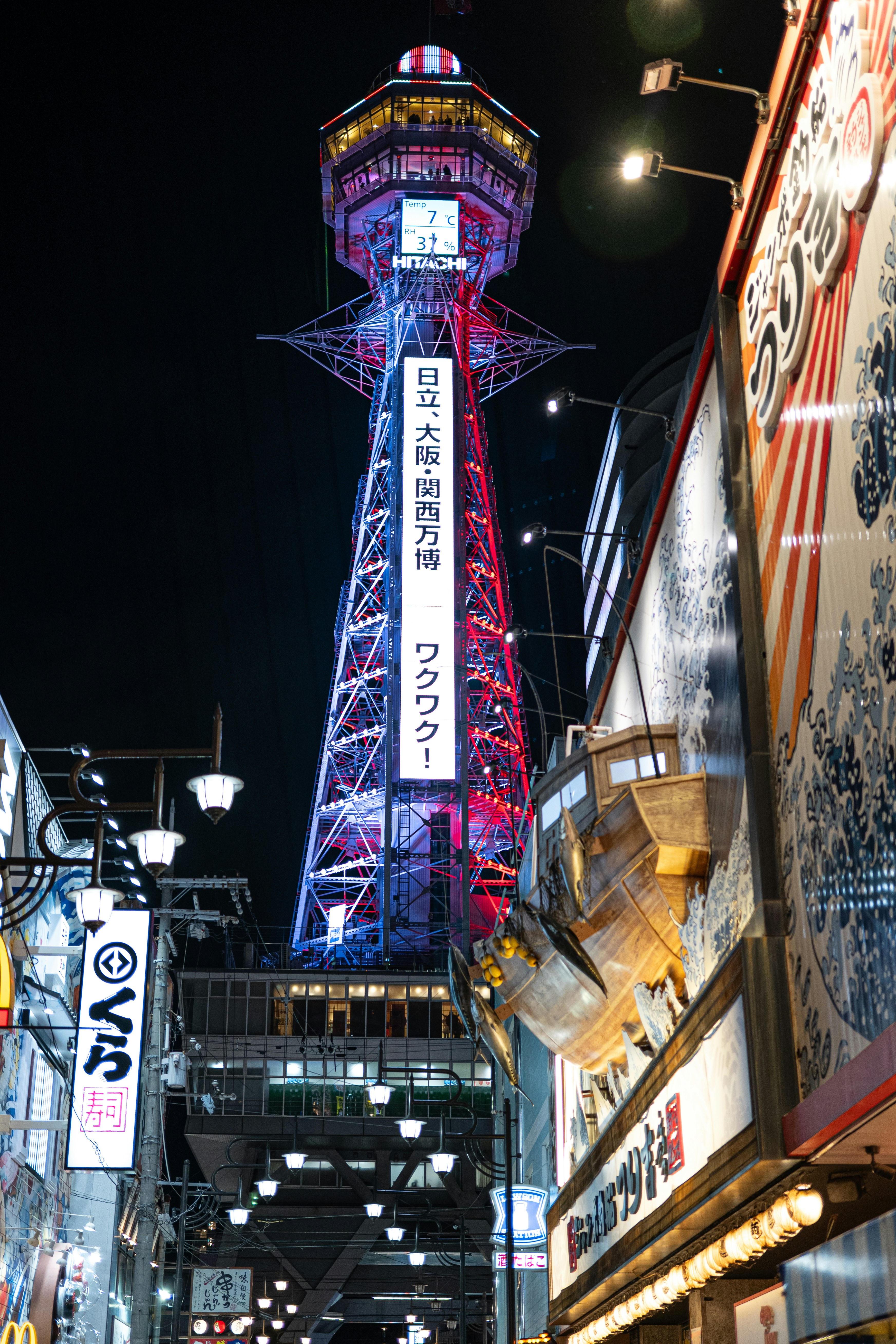 Neon beacon: skyscraper tower rising above a bustling Osaka street at night