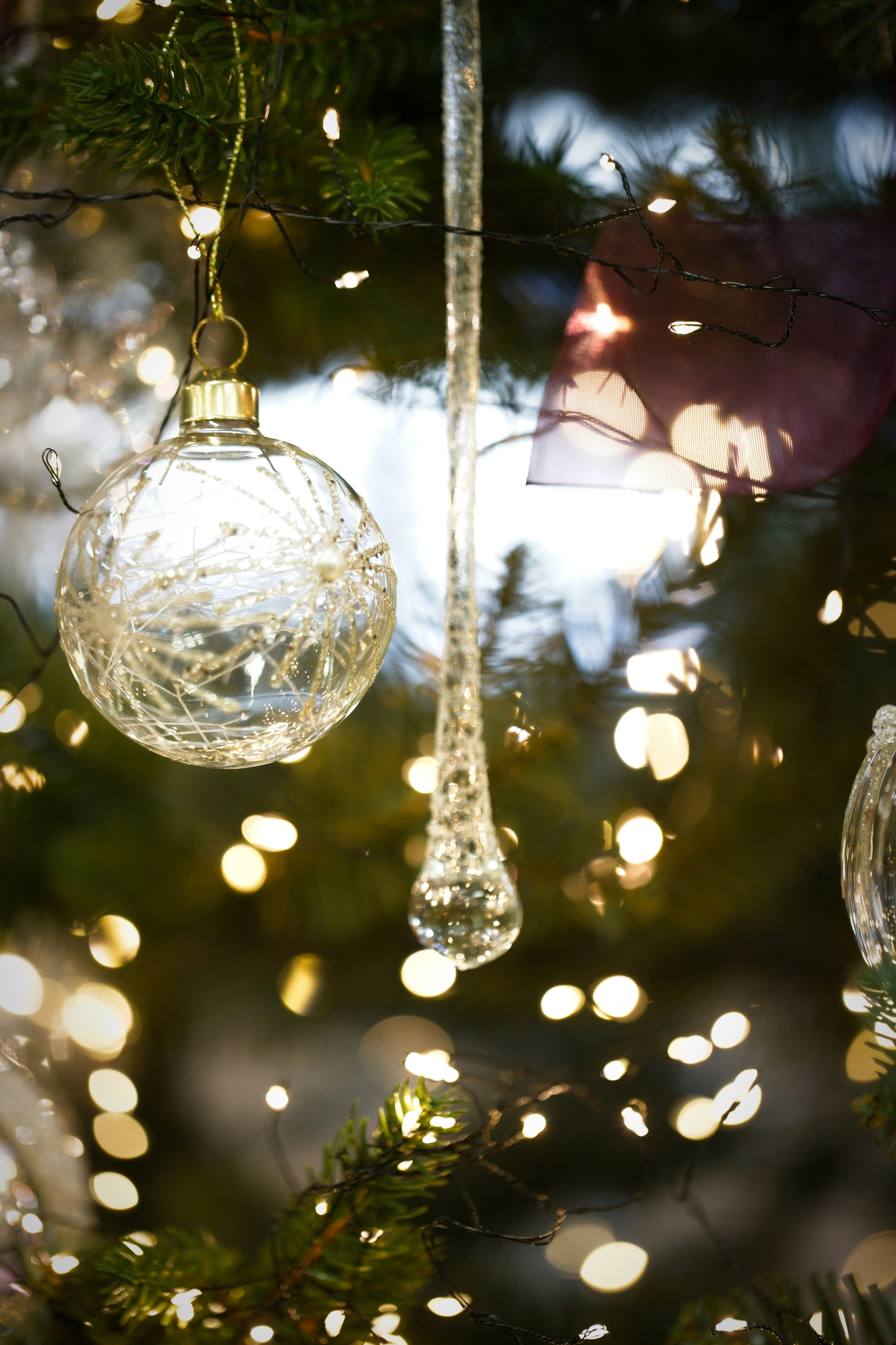 Close-up of glass Christmas ornaments and fairy lights hanging on festive tree
