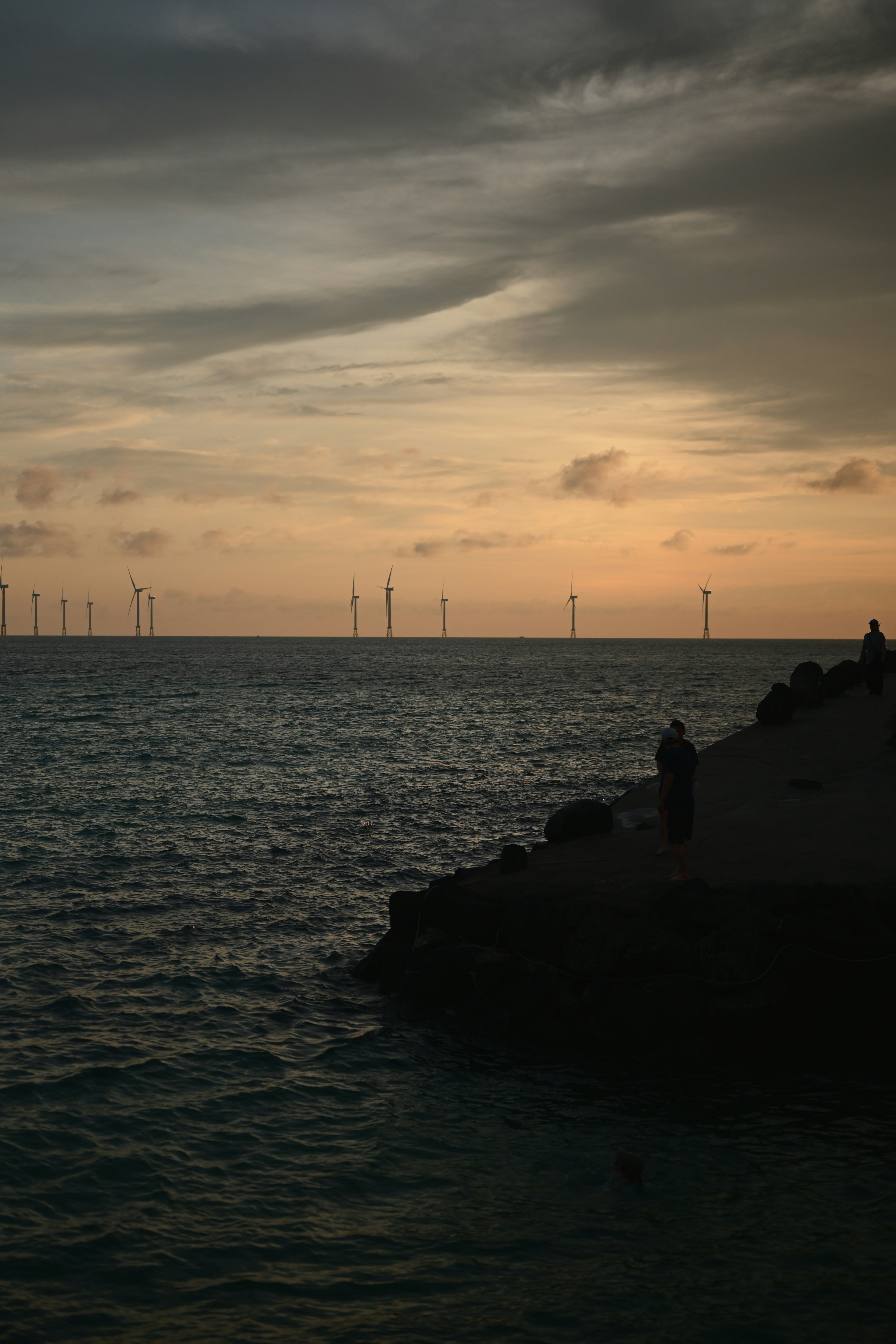Sunset over a Quiet Breakwater with Distant Wind Turbines