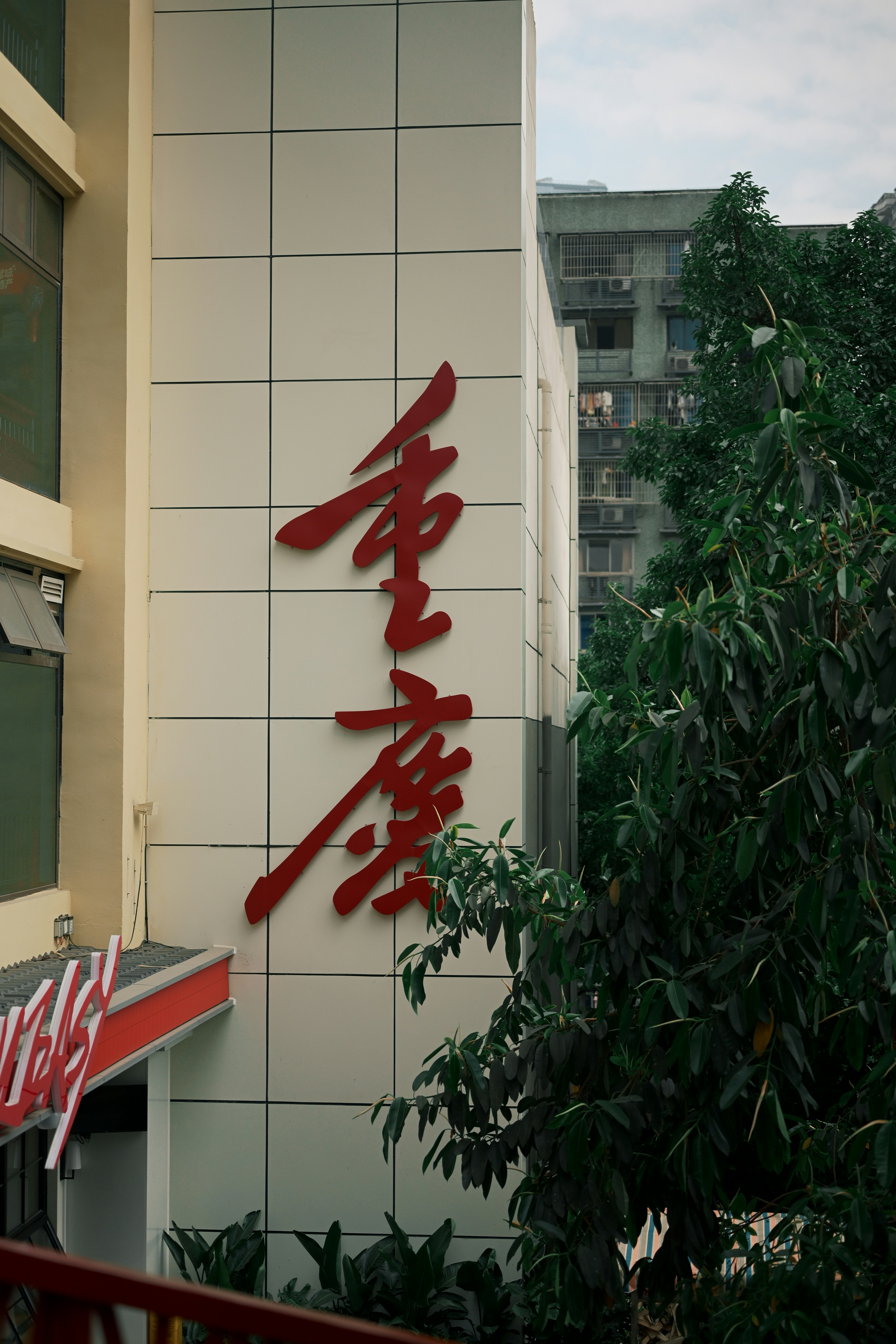 Vertical Red Characters on Modern Facade with Lush Greenery