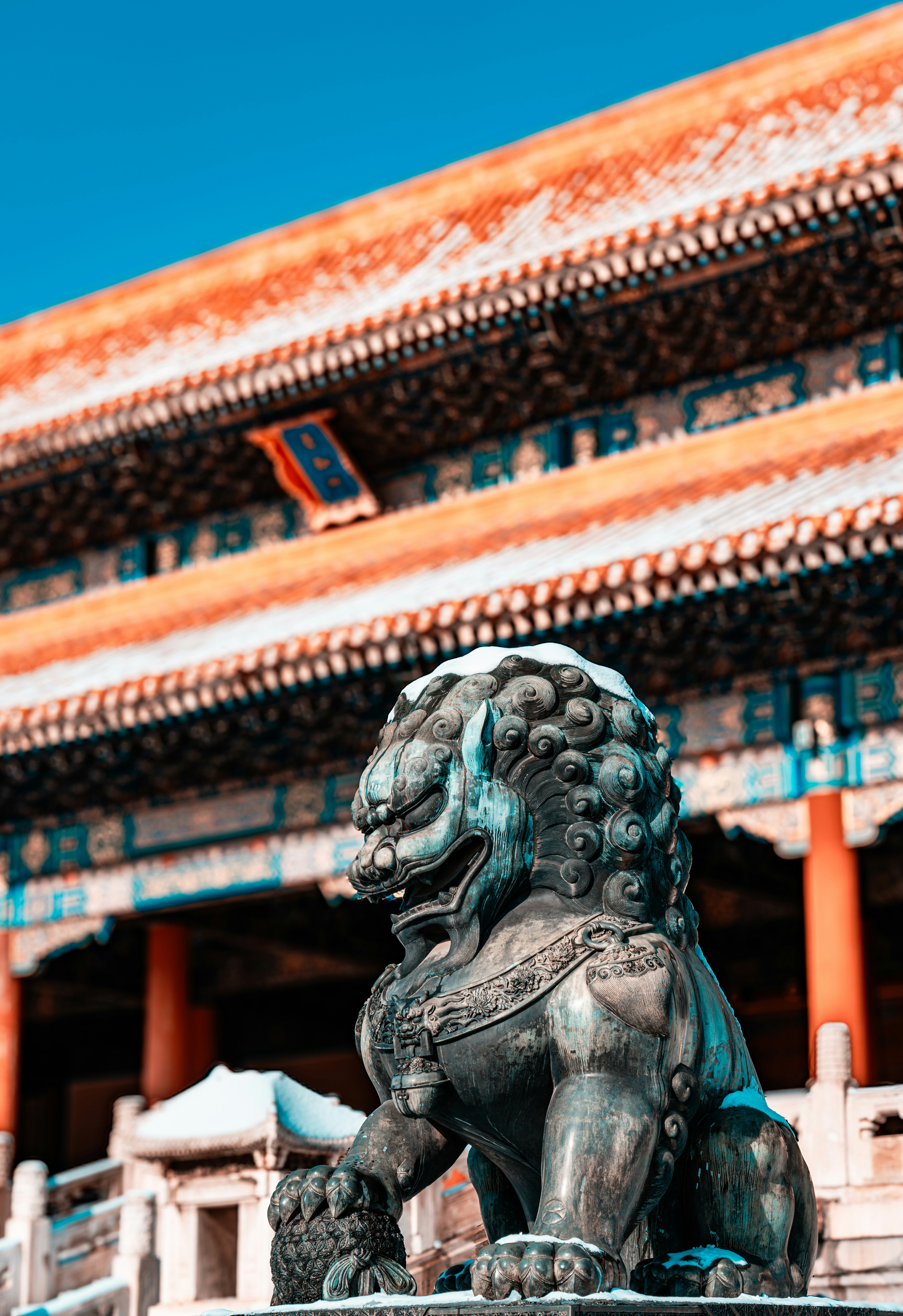Stone lion statue in front of snowy traditional chinese building