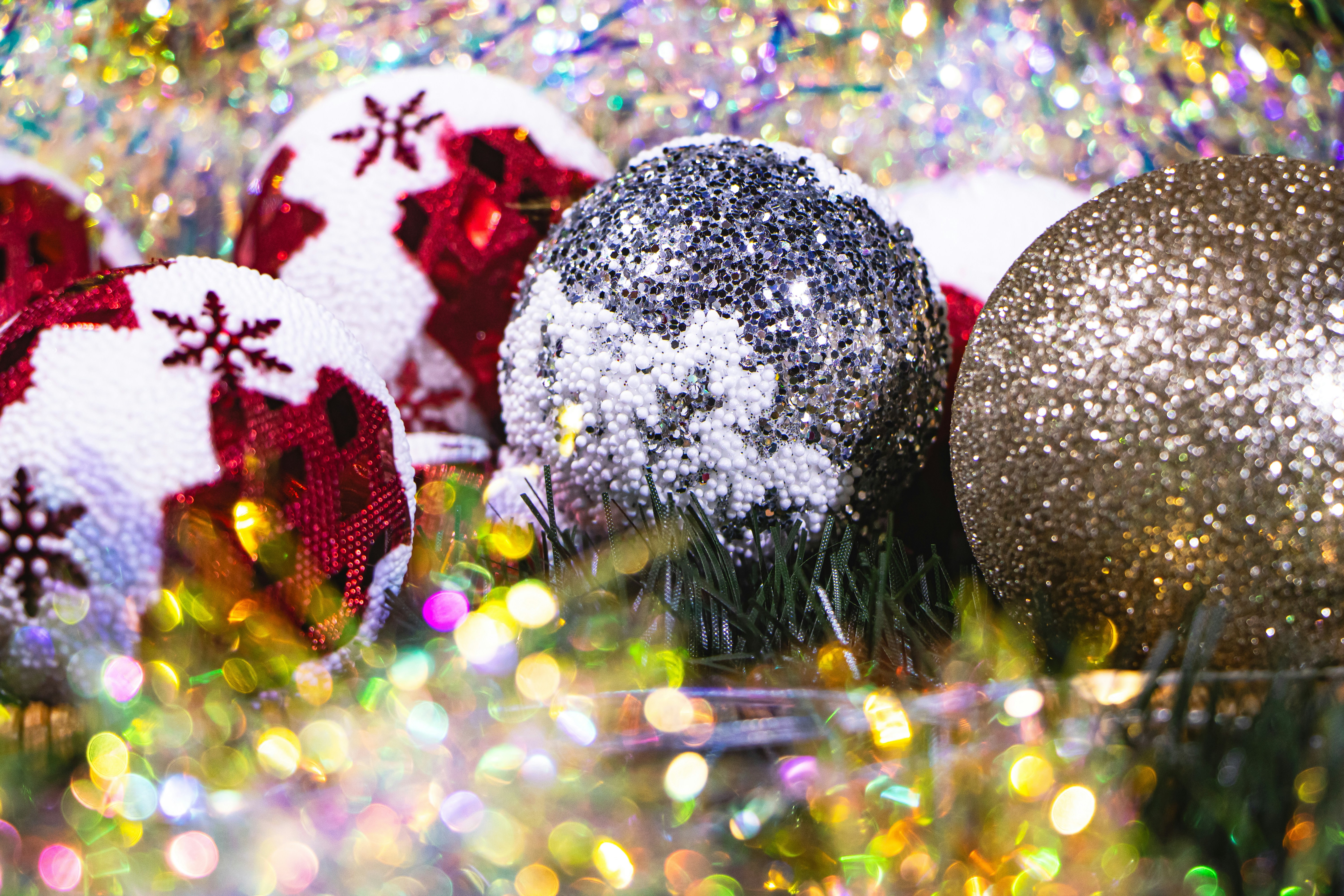 A vibrant cluster of Christmas ornaments—red, white, gold, and silver—nestled among shimmering tinsel and festive lights. Snowflake patterns, glittery textures, and cozy holiday motifs evoke the joyful spirit of the season in dazzling detail.
