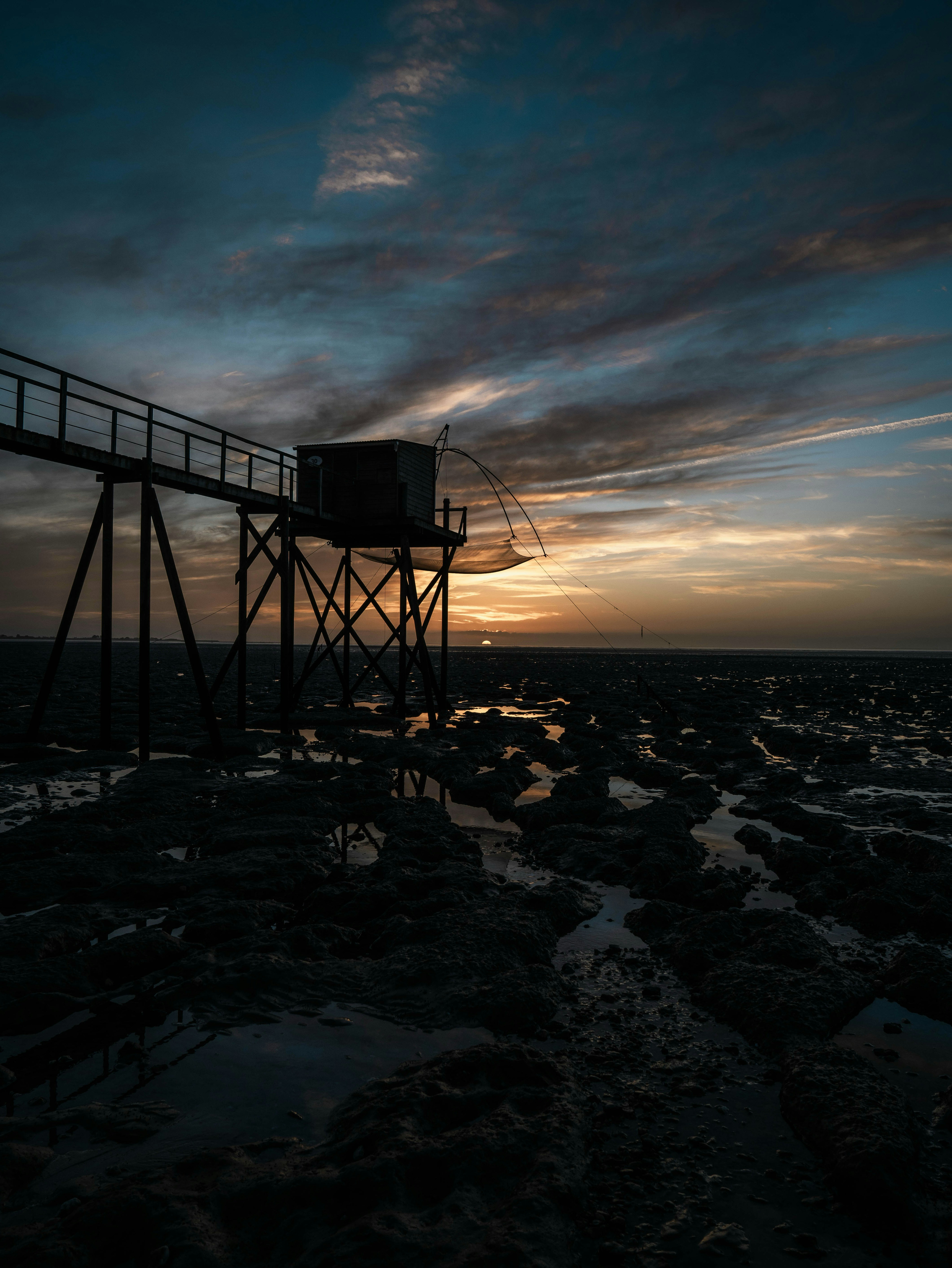 Sunset Over the Pier: Silhouetted Net and Tide-Pocked Shore