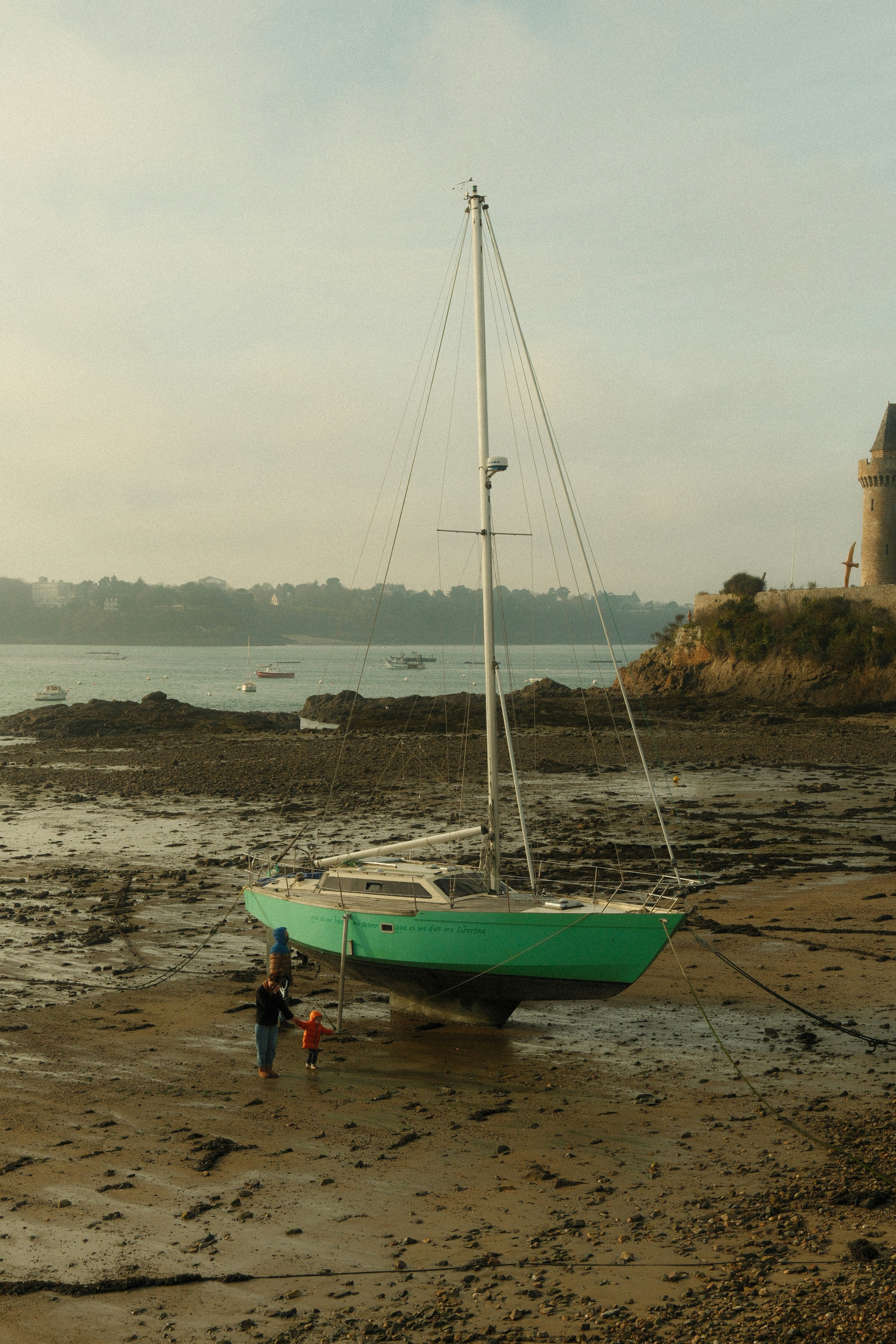 Green-hulled sailboat resting on a tidal beach with a small family nearby
