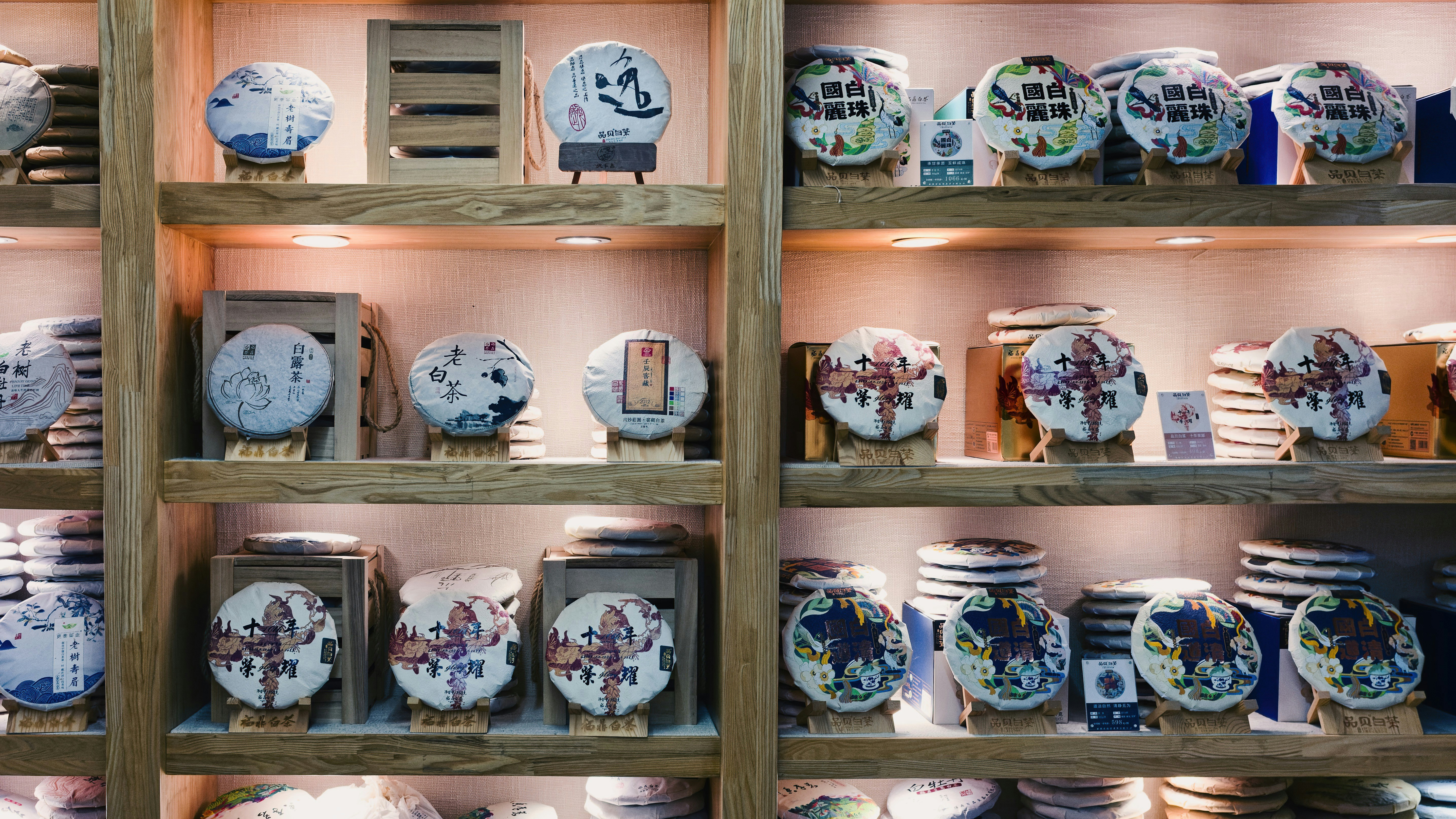 Display of various tea cakes in a store showcasing different designs and packaging - A store features many tea cakes stacked on wooden shelves. Each cake has unique designs and labels. The display is well-organized and bright, attracting customer attention.