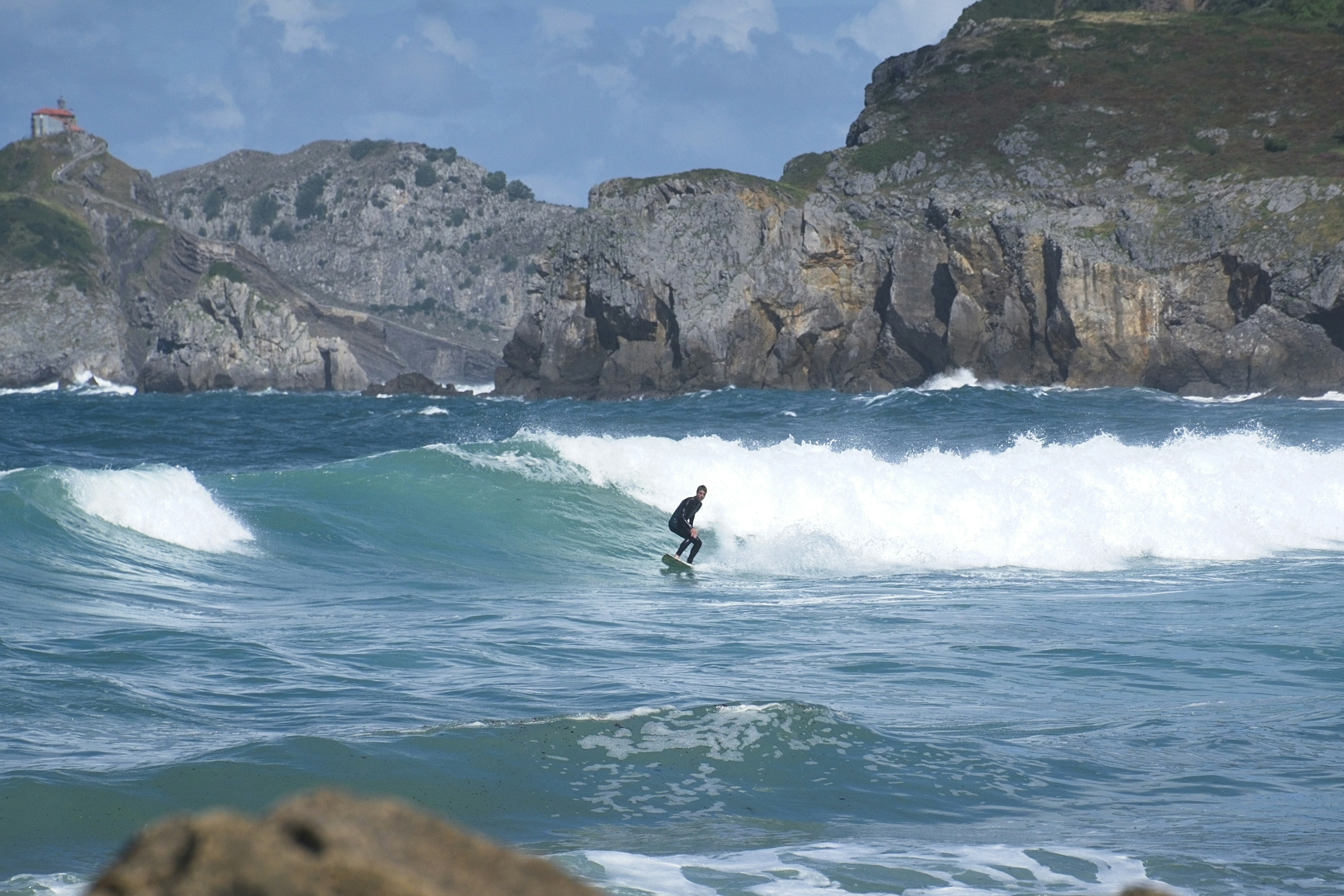 Surfer on a Cresting Wave Beneath Rugged Coastal Cliffs