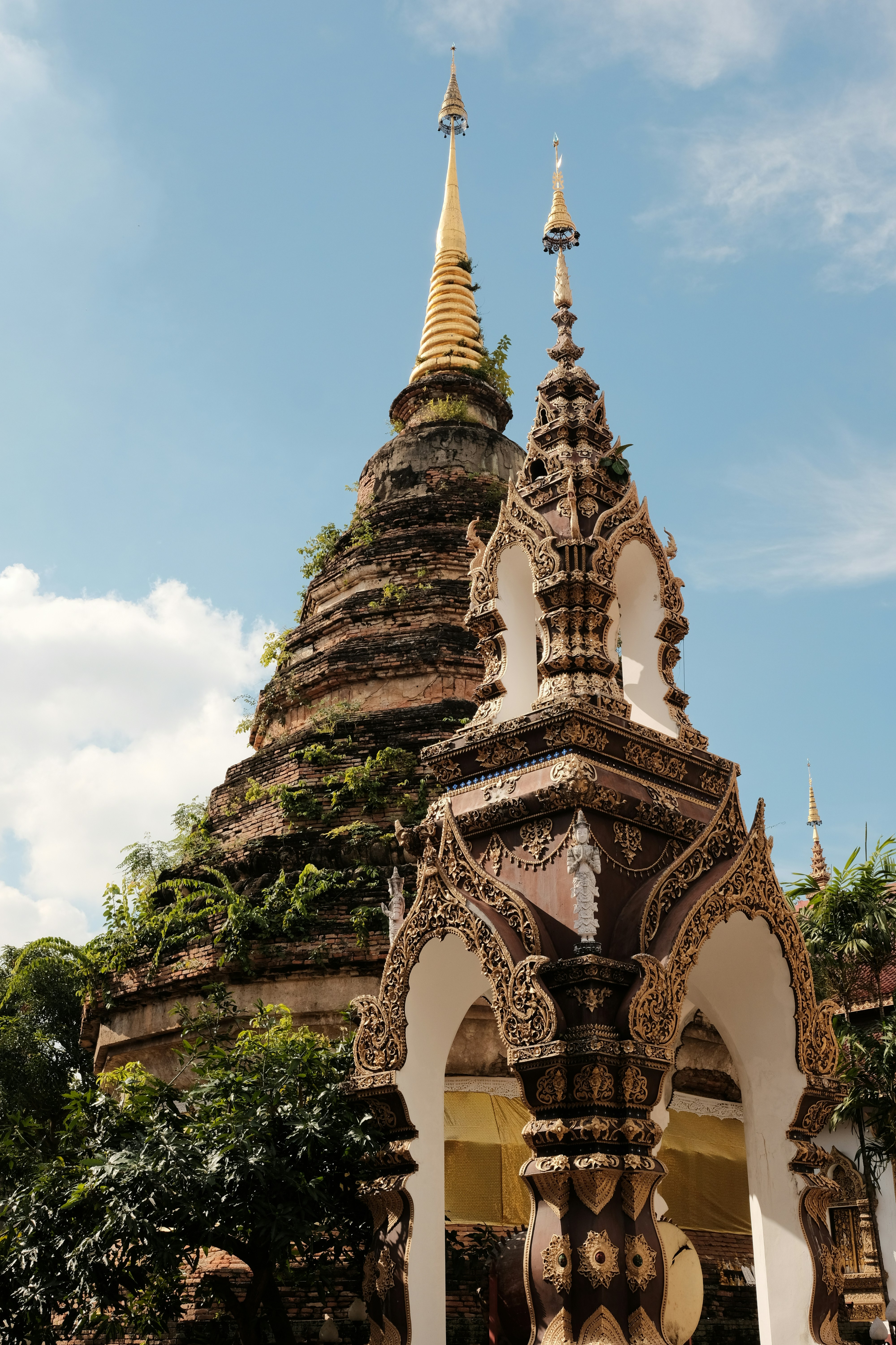 A temple arch in front of an old brick chedi crowned with golden spires in Chiang Mai, Thailand.