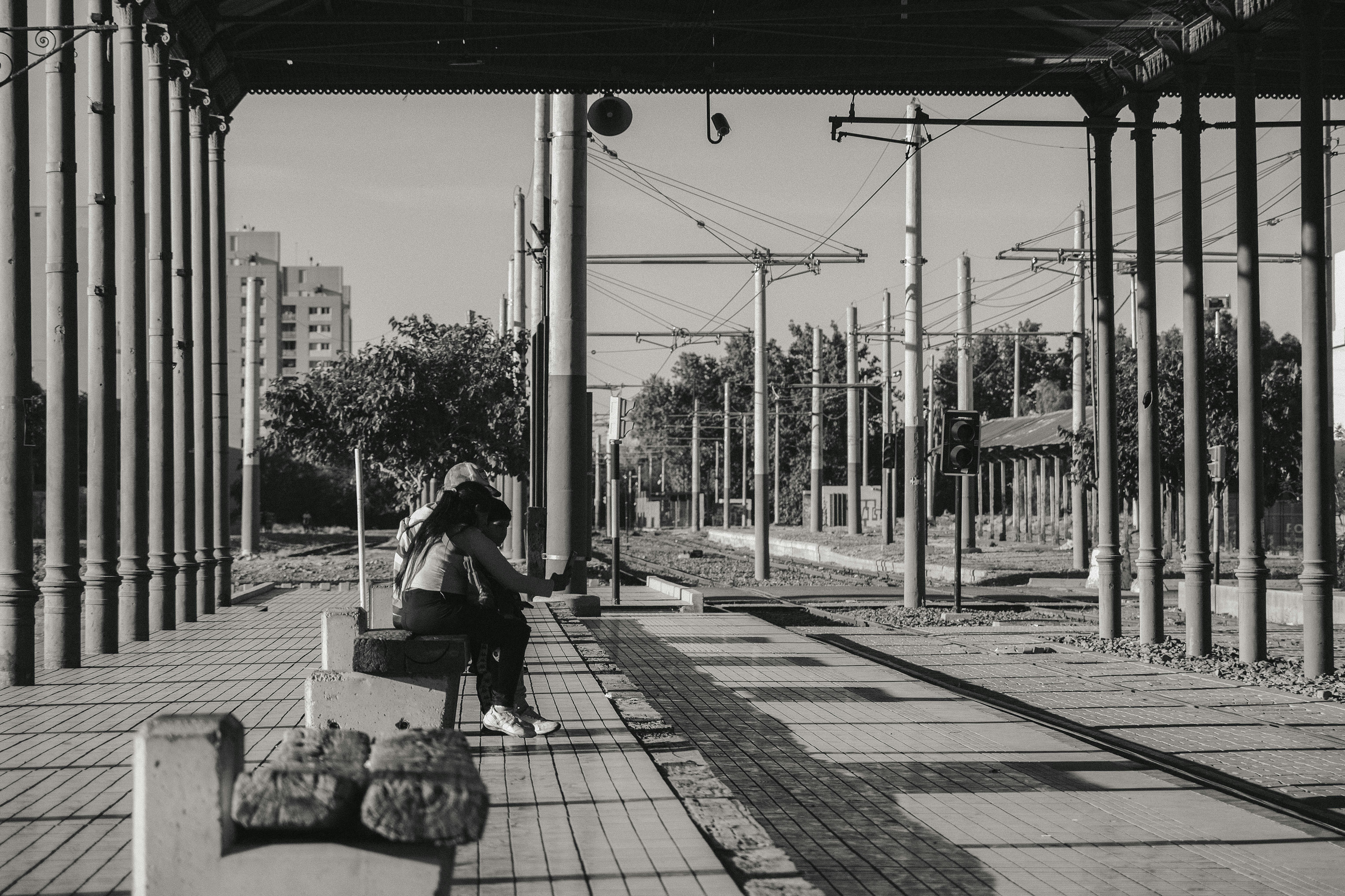 Quiet platform, loud shadows: a solitary traveler waits under a station canopy