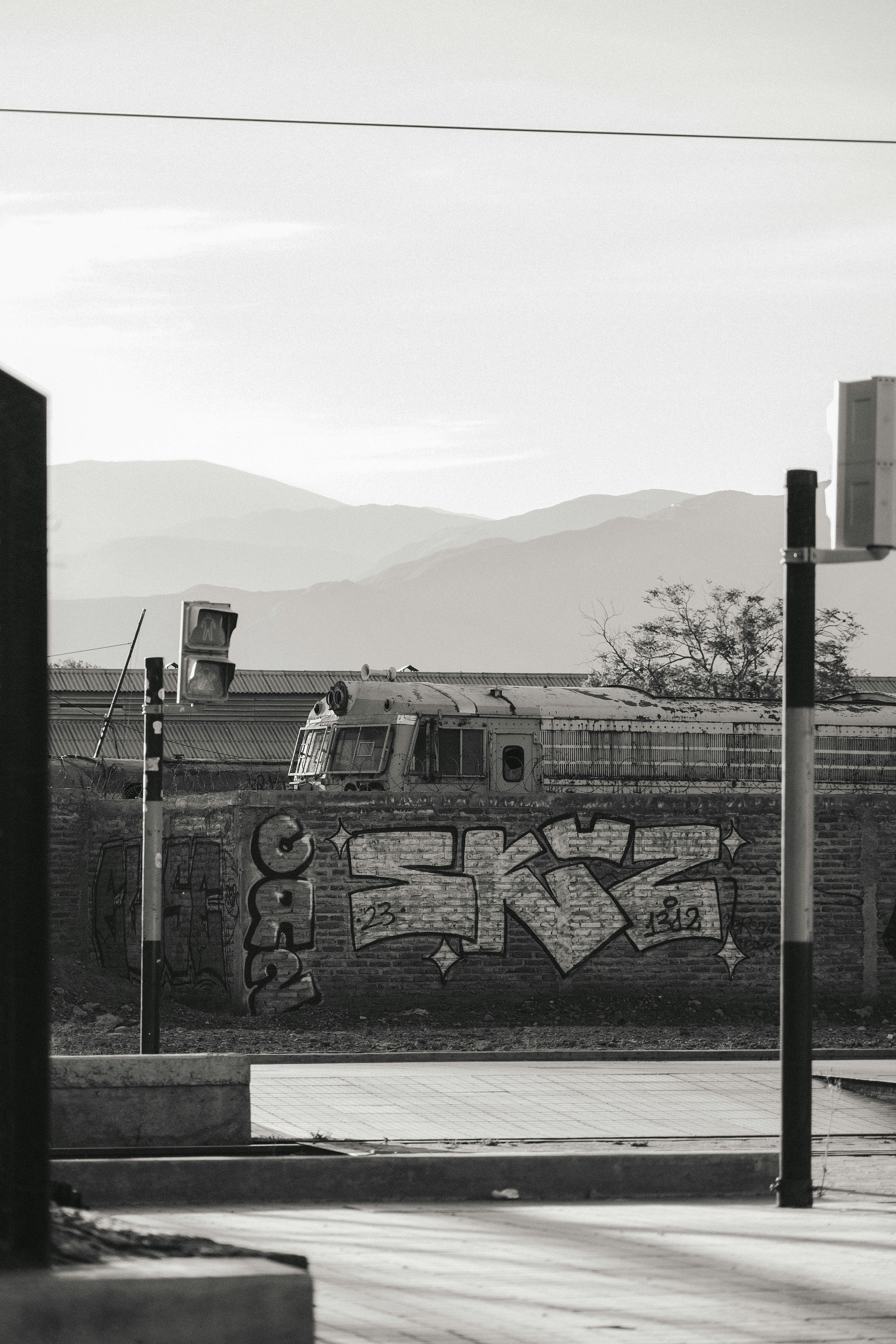 Urban train yard scene with graffiti-covered wall and a train peeking above, framed by foreground platforms and utility poles.