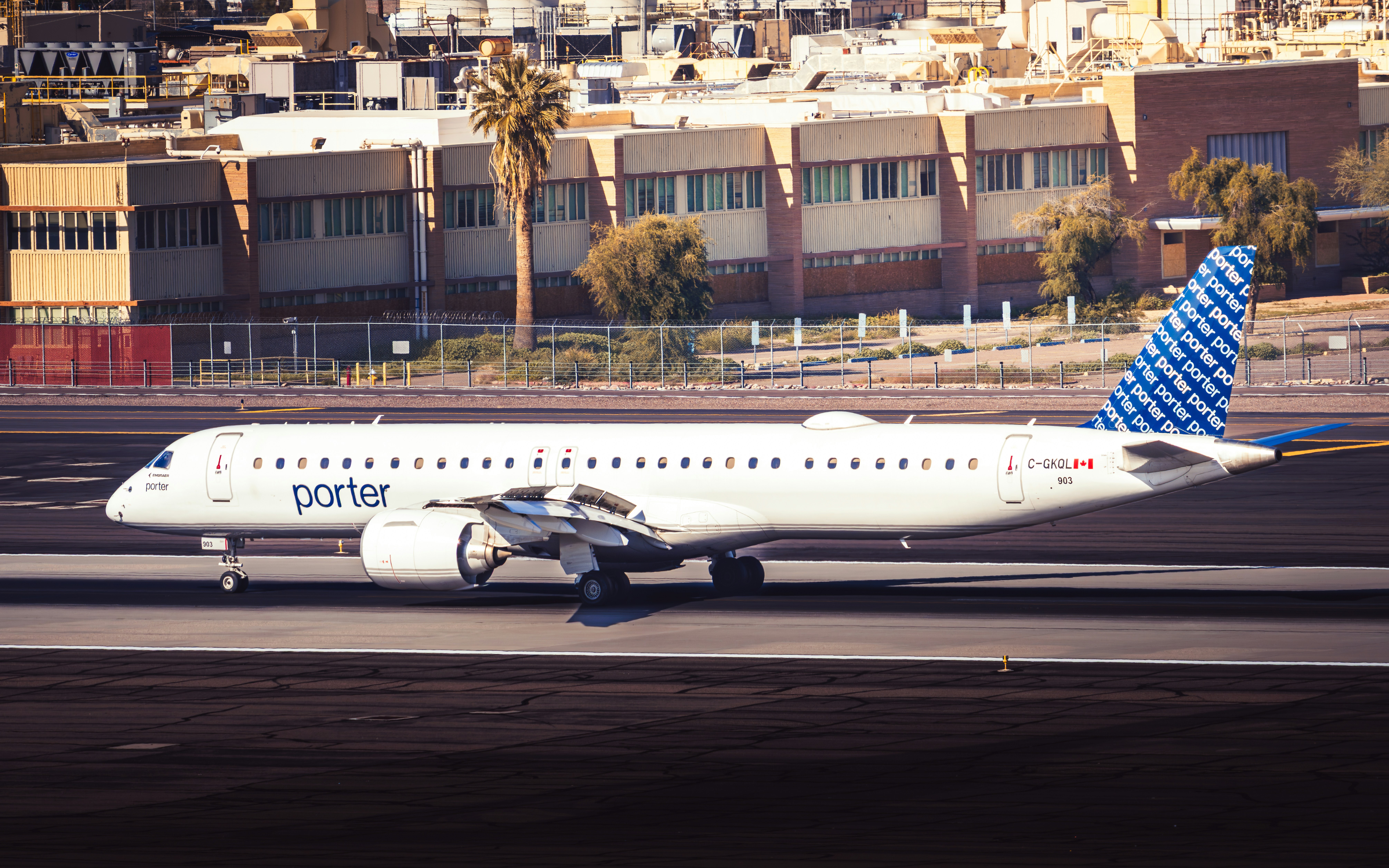 Porter Boeing on a sunlit taxiway under a row of low-rise buildings