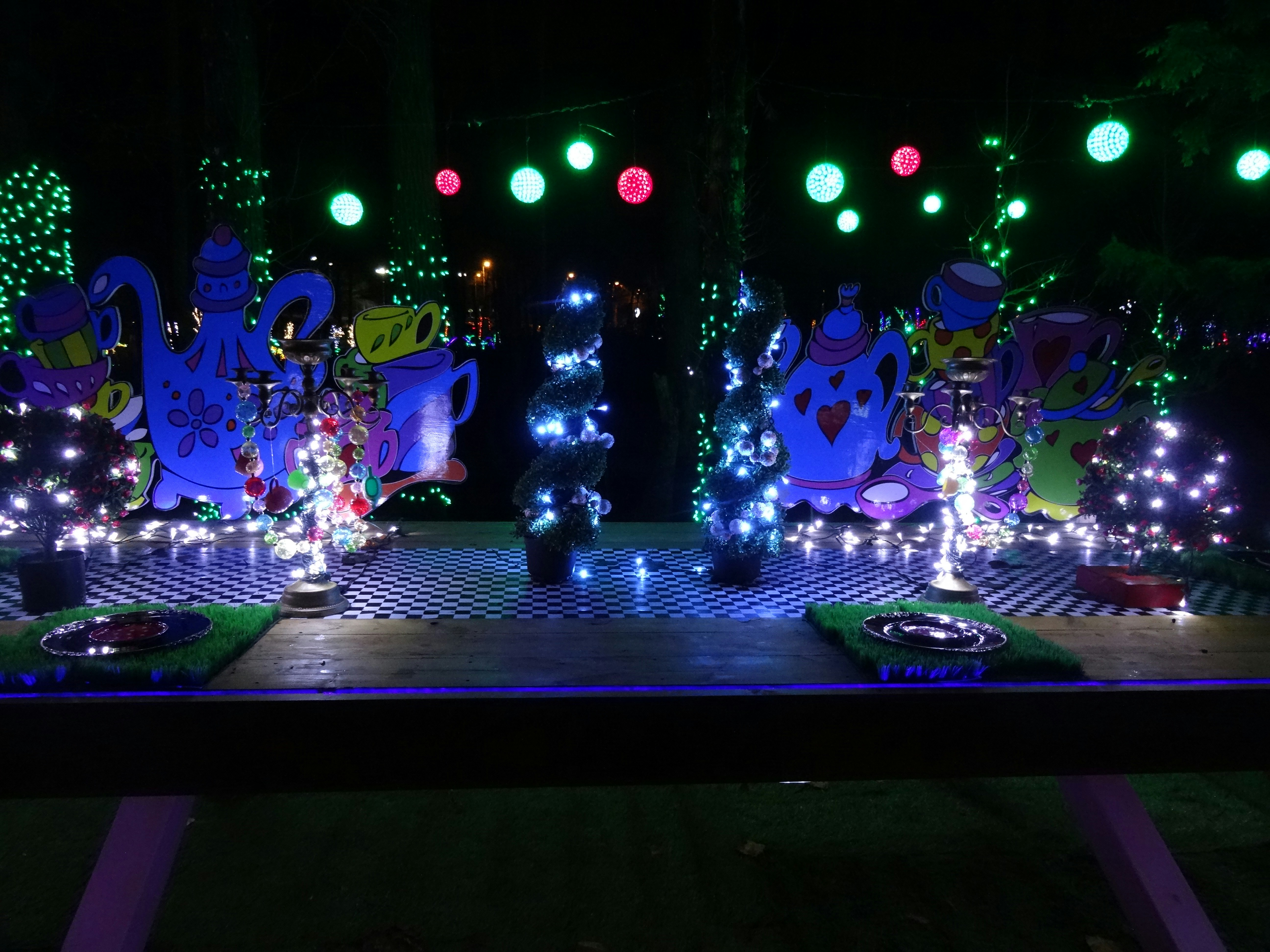 Whimsical tea party decorations illuminated by fairy lights at night.