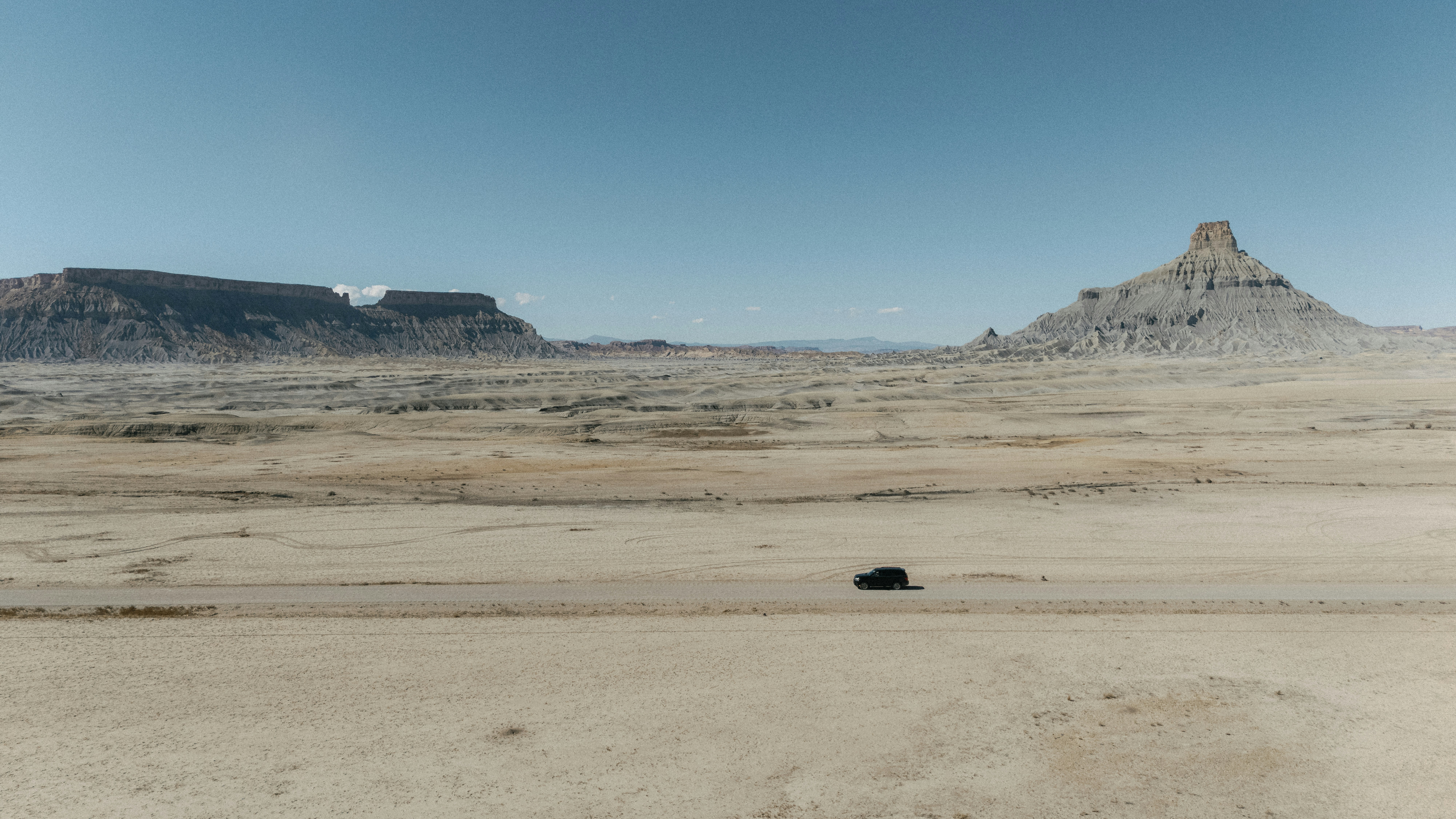 Car in the vast desert beneath sculpted mesas