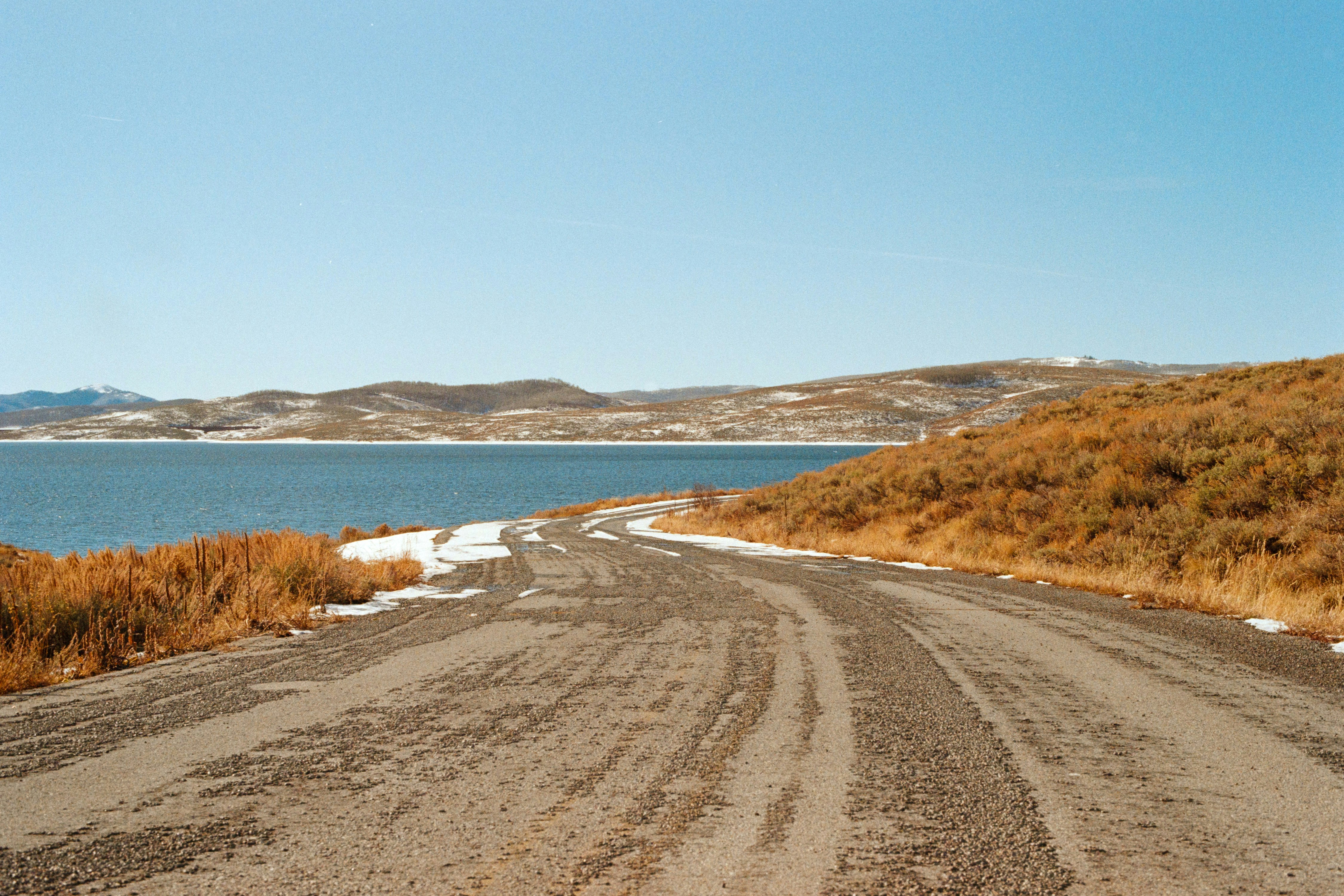 Winding dirt road beside a calm lake under clear sky photo – Free ...