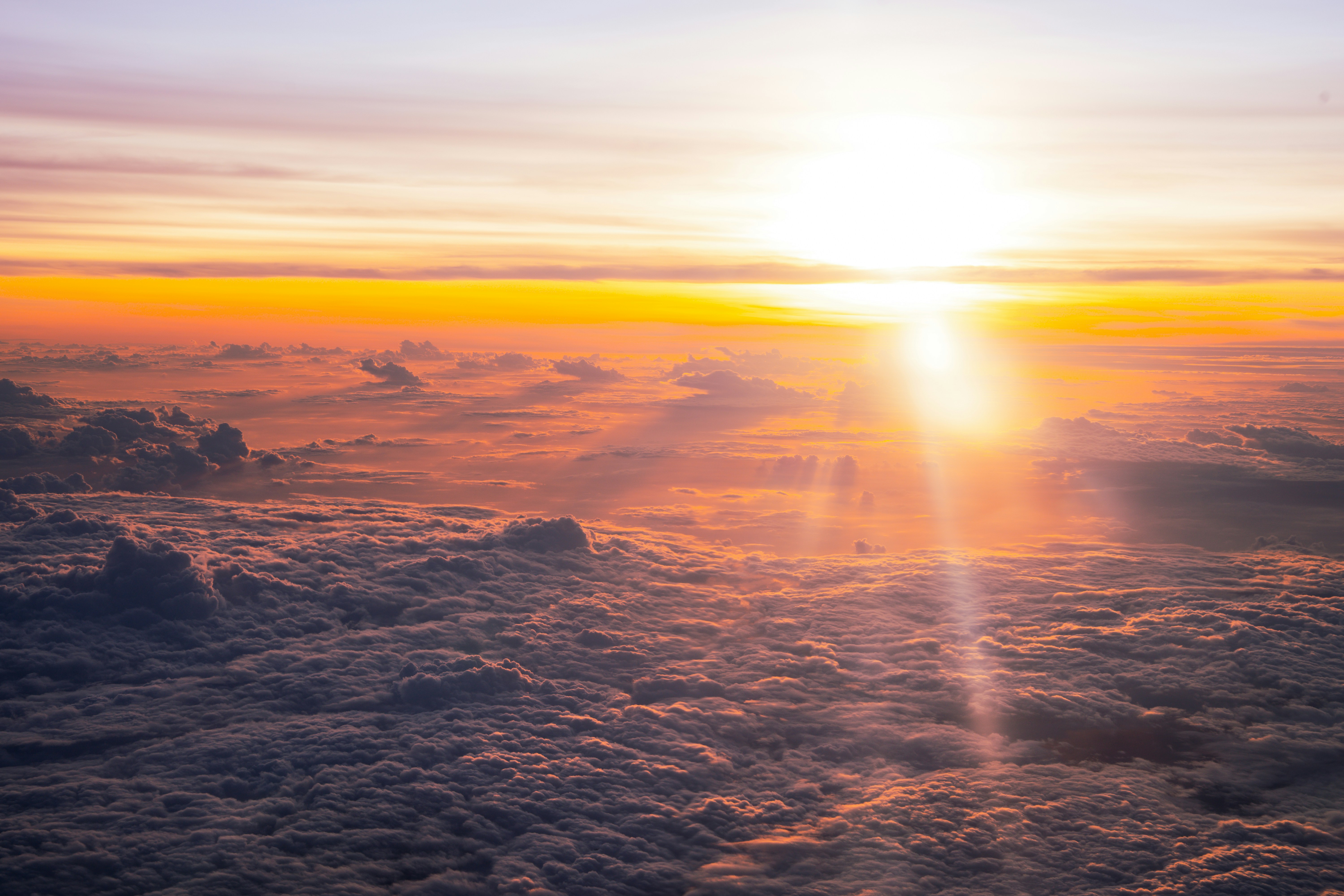 Golden sunlight hitting the horizon line above a thick layer of clouds. A dramatic nature shot showing the vast atmosphere during golden hour