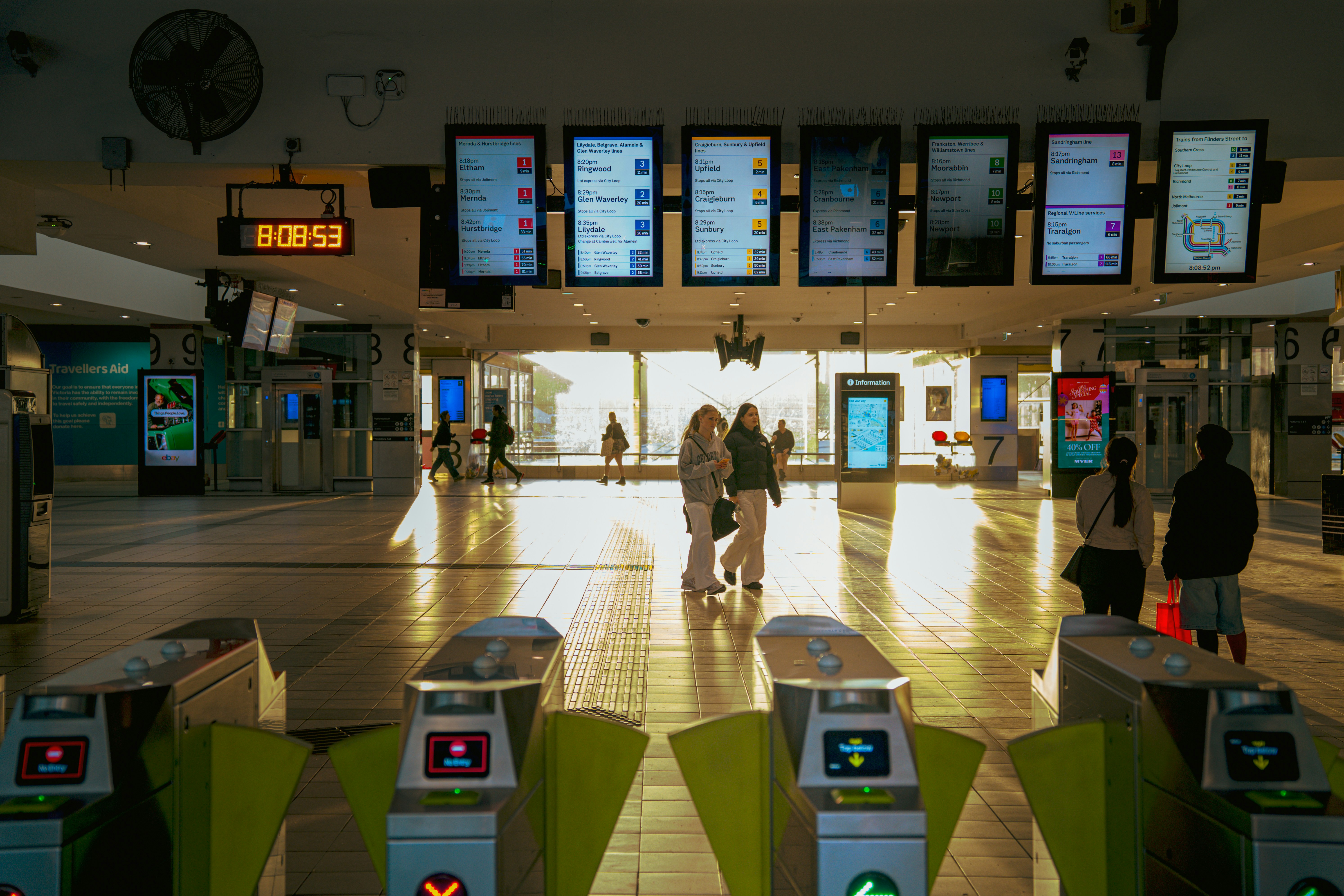 Commuters walking through the ticket gates at Flinders Street Station in Melbourne, illuminated by the warm glow of sunset