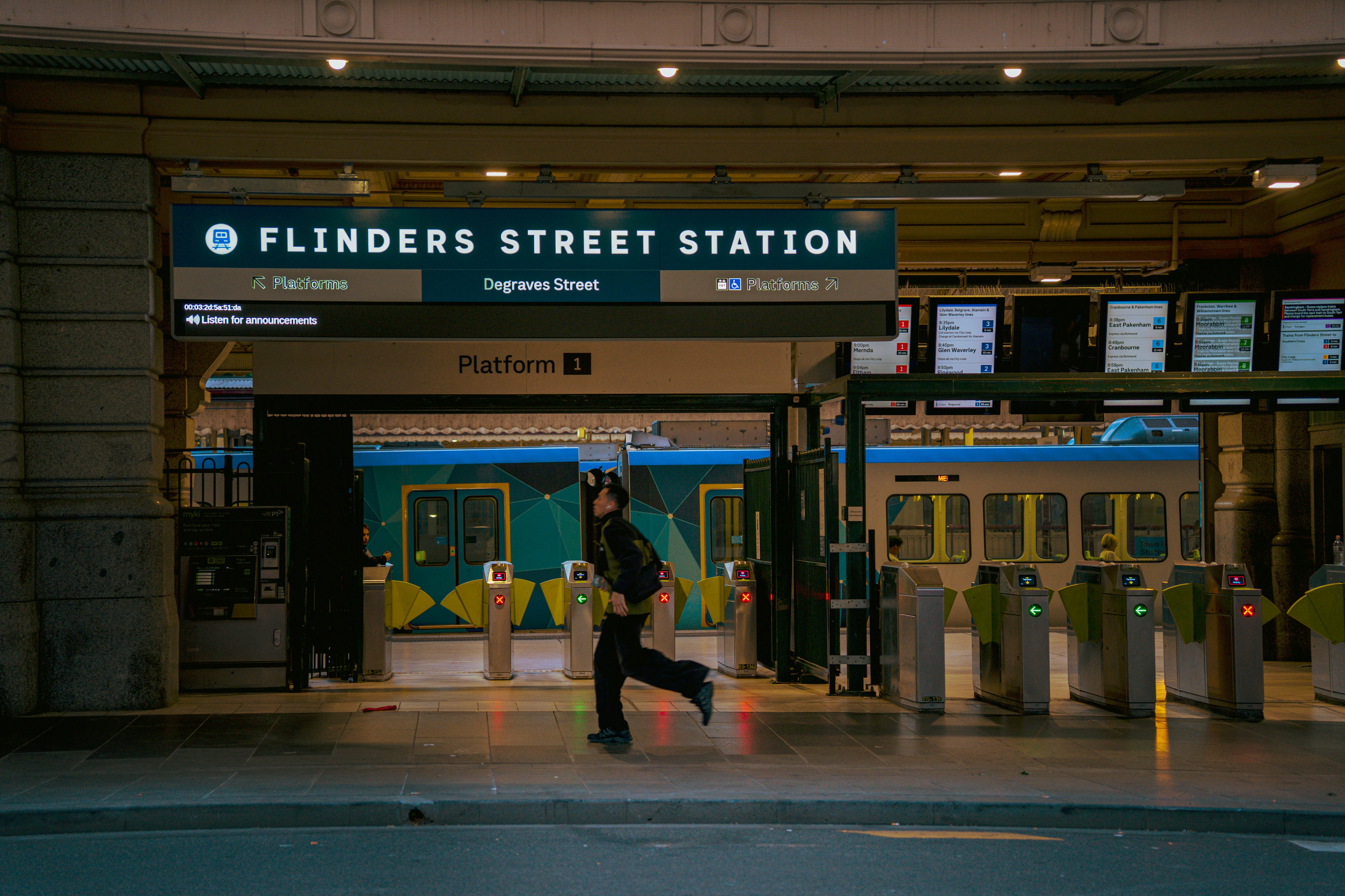 Commuters walking through the ticket gates at Flinders Street Station in Melbourne, illuminated by the warm glow of sunset