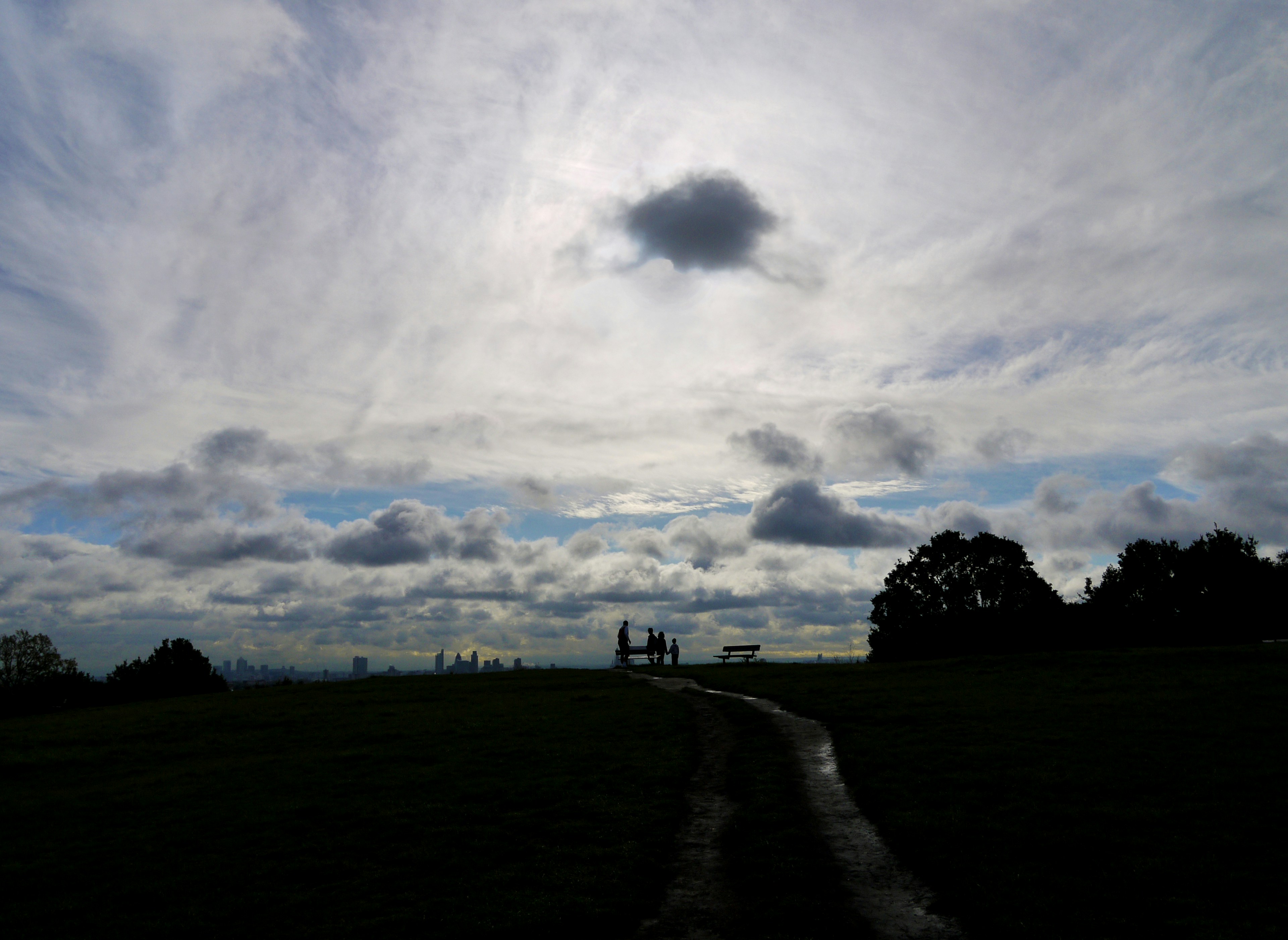 Silhouetted figures walk on a path under cloudy sky.