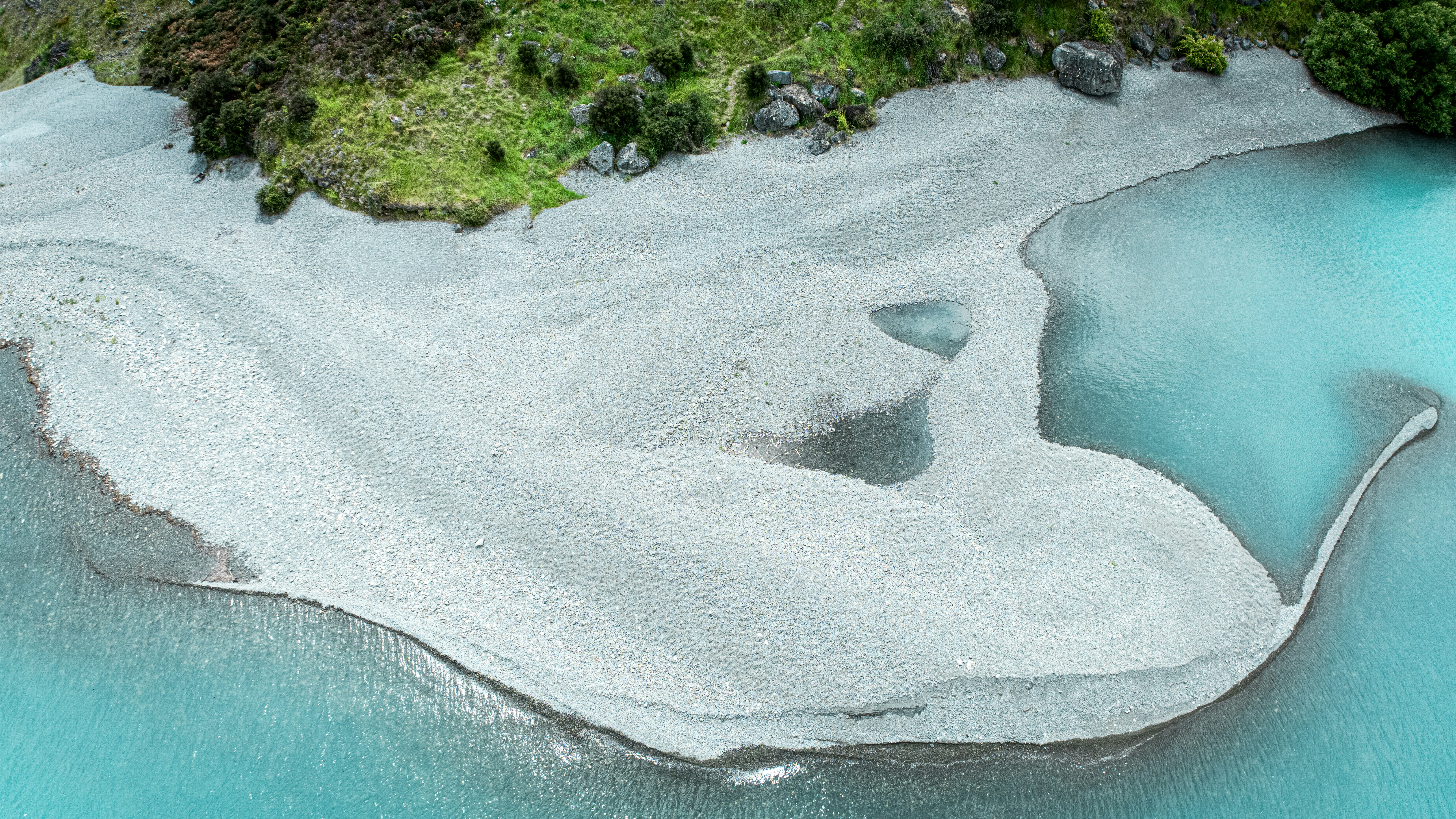 Vivid turquoise water frames a winding white-sand shoreline and rocky greenery, highlighting a tranquil coastal scene.