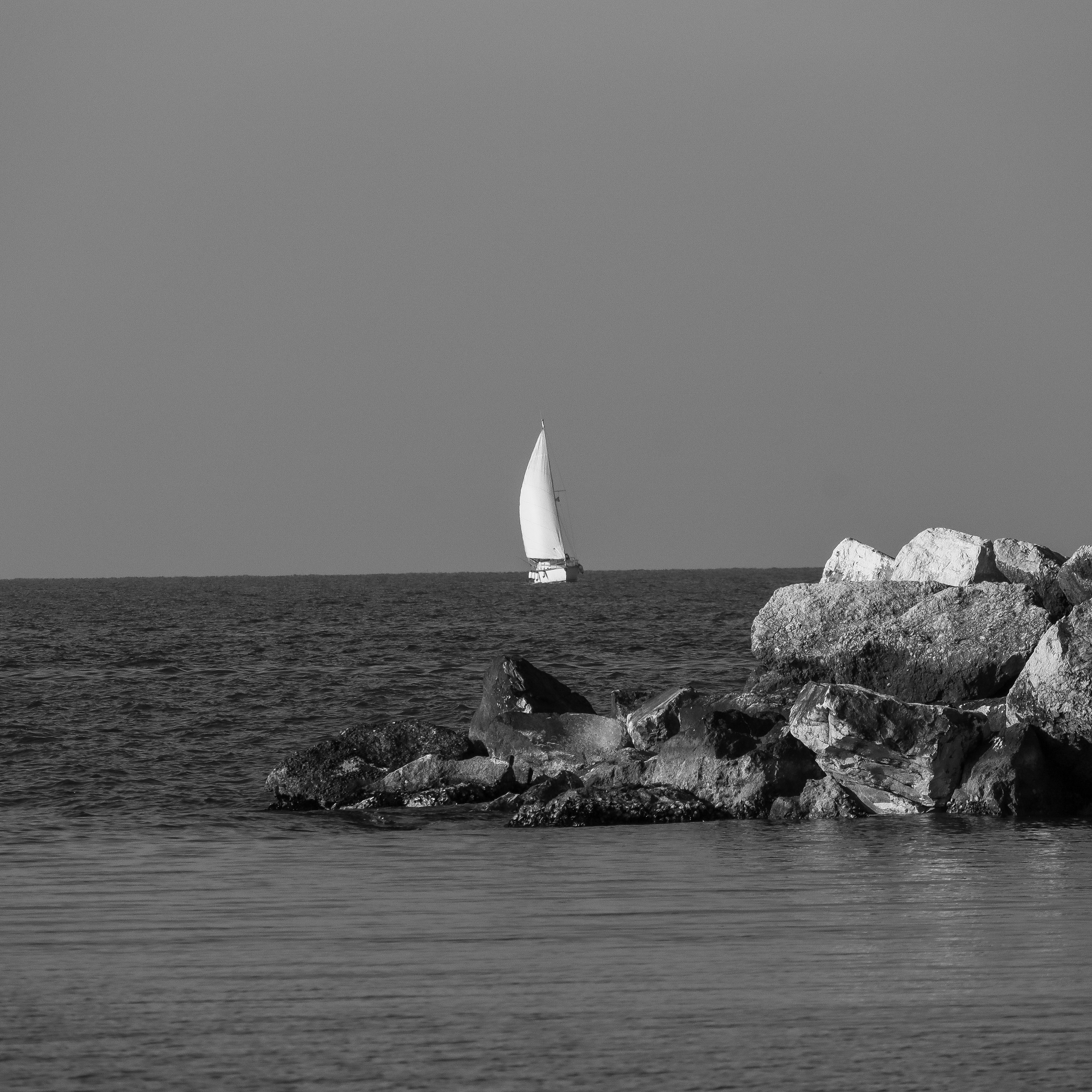 Grey Horizon: A Lone Sailboat Against The Rocked Seascape