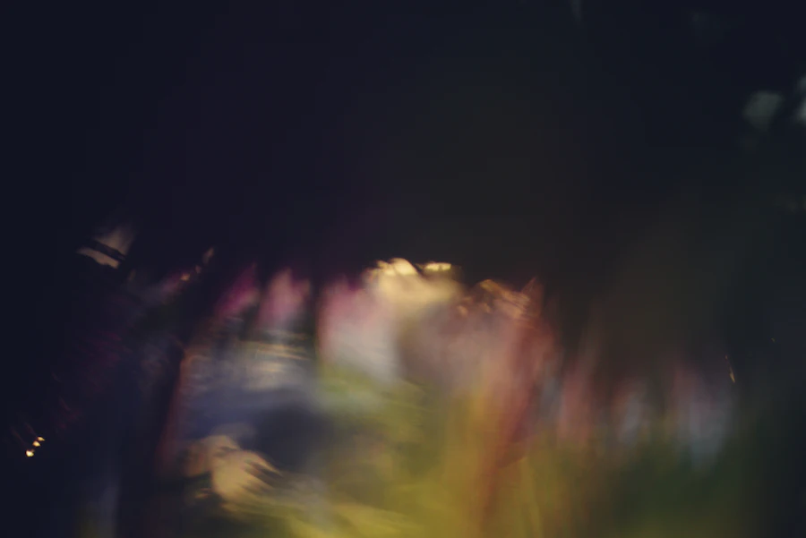 Vivid, abstract blur of a garden scene with greens, yellows, and pinks; the composition emphasizes motion and color rather than a defined subject. This is a photographic capture, not a drawing or painting.